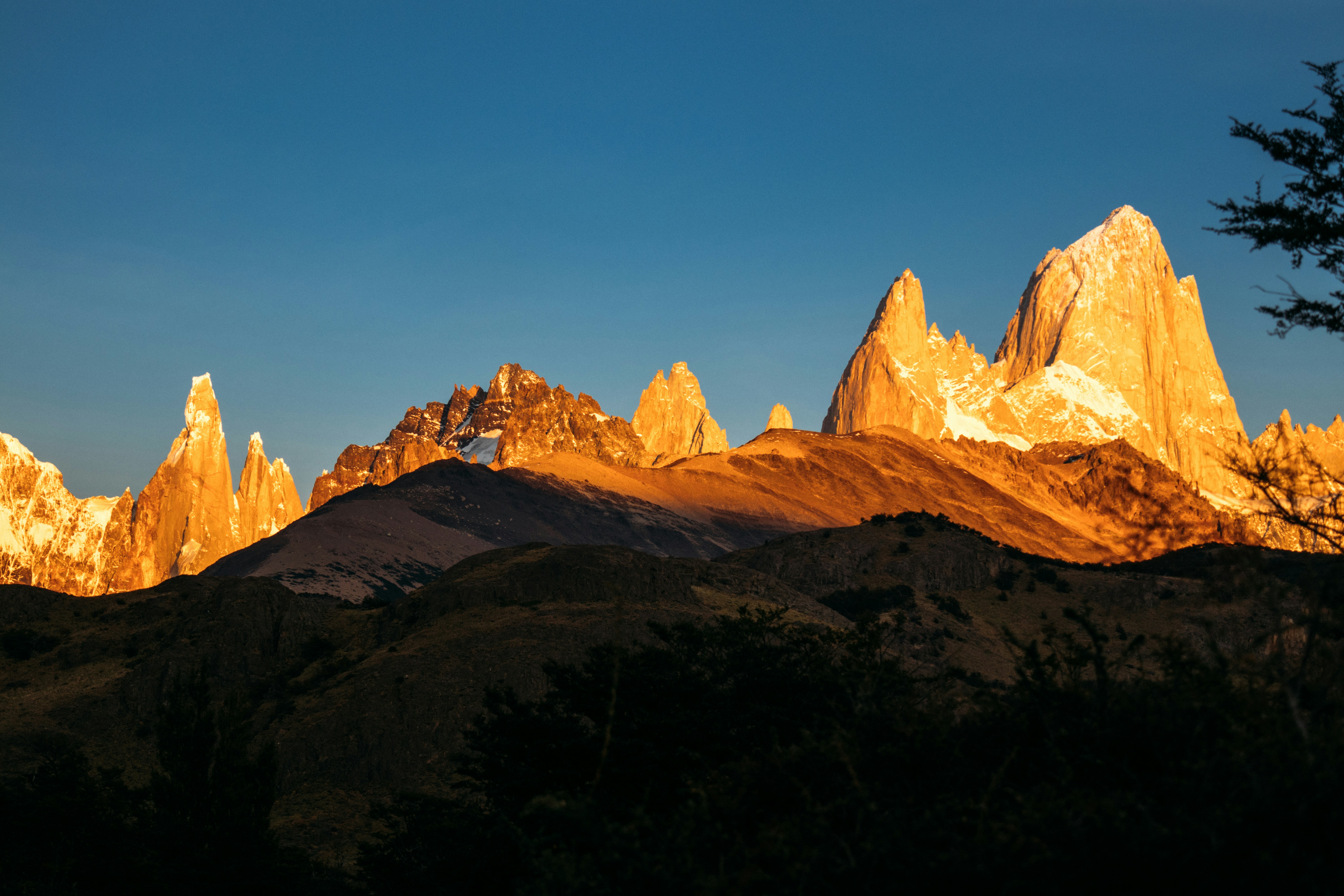 Golden light illuminates majestic mountains against a clear blue sky ...