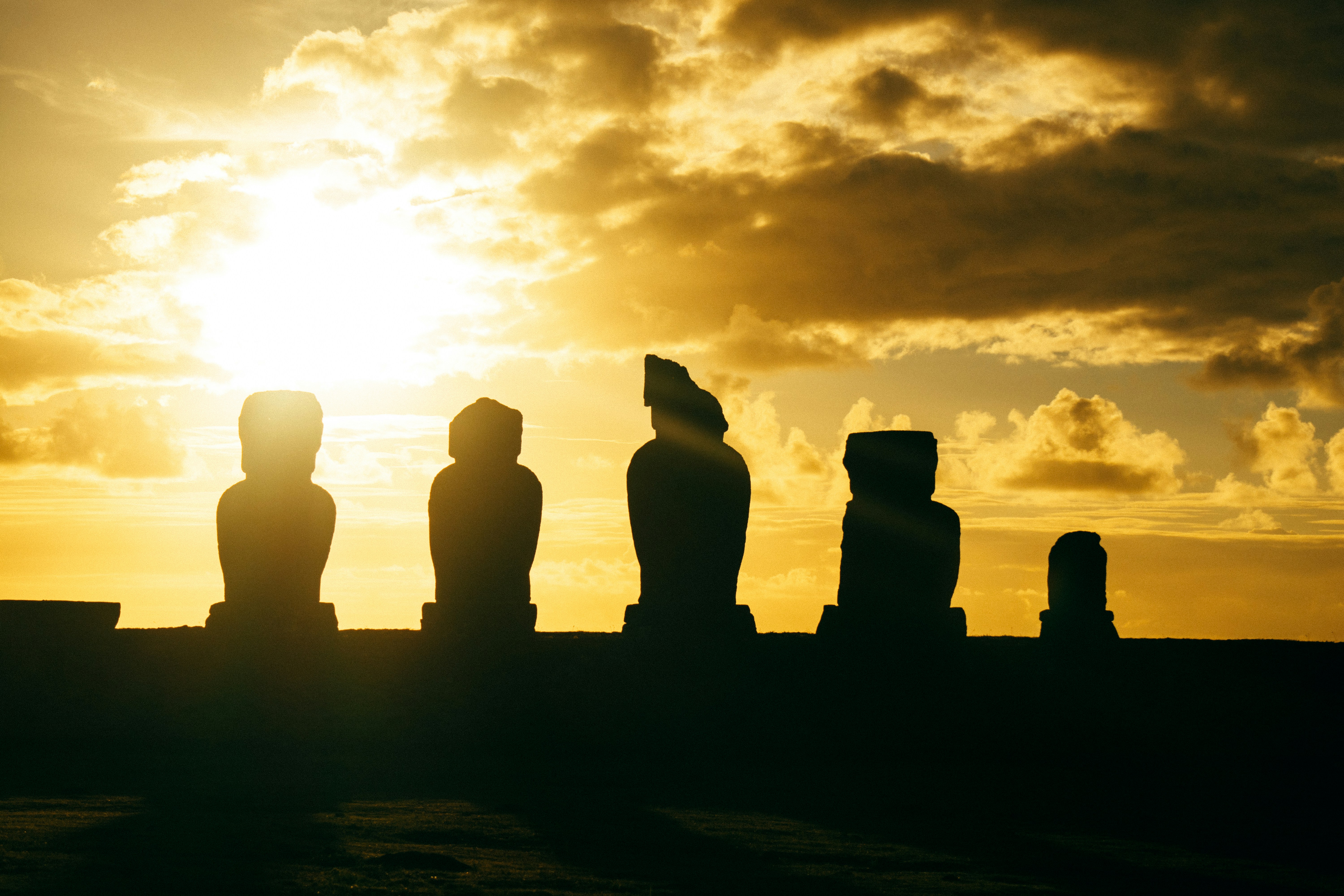Silhouetted Moai-esque Figures: A Golden Horizon at Dusk