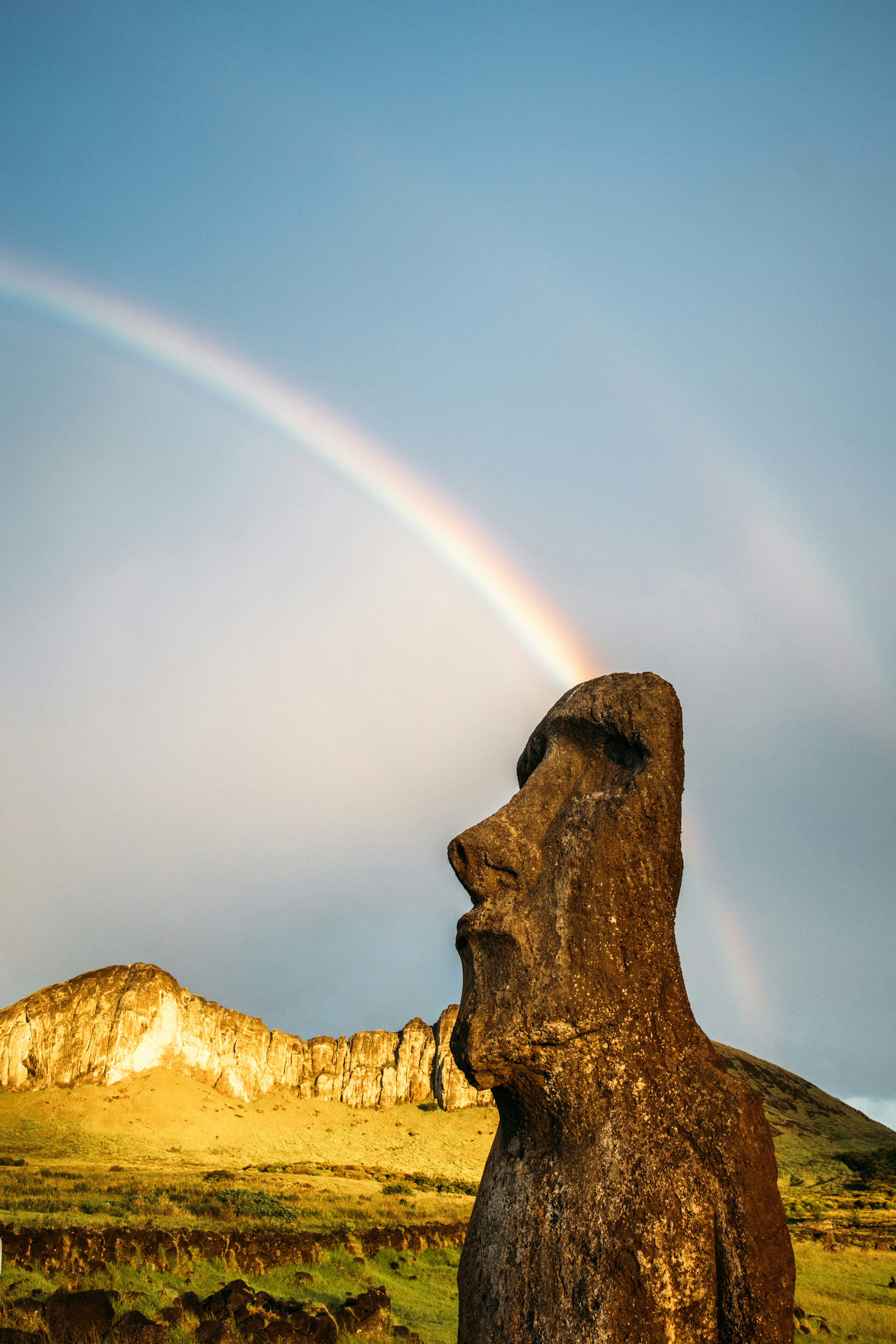 Ancient Stone Figure Beneath a Double Rainbow over Quiet Plains