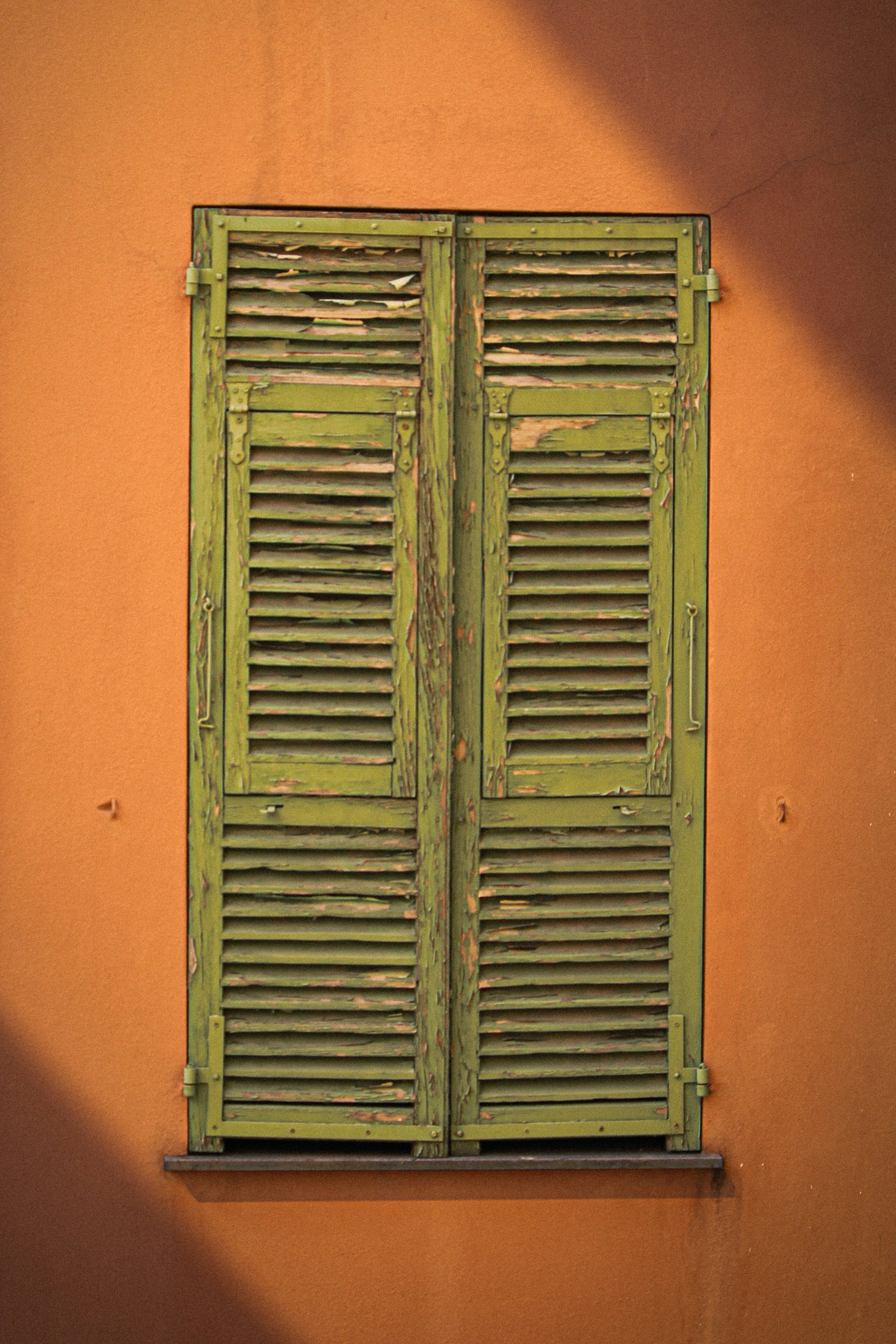 Green Shutter Against Burnt Orange: A Weathered Door in Quiet Light
