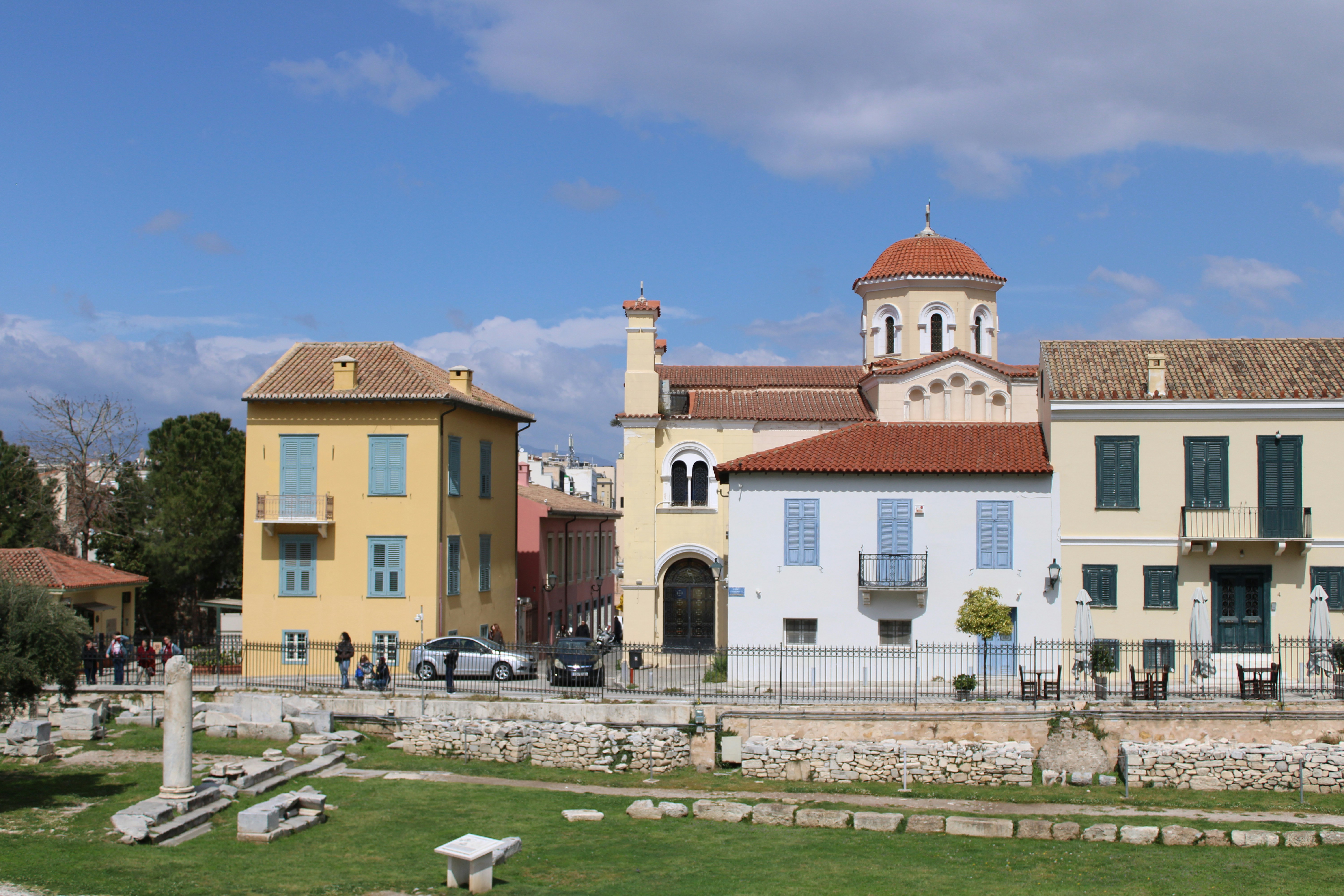 Row of pastel houses with a small courtyard and a stone wall along a tranquil waterfront.