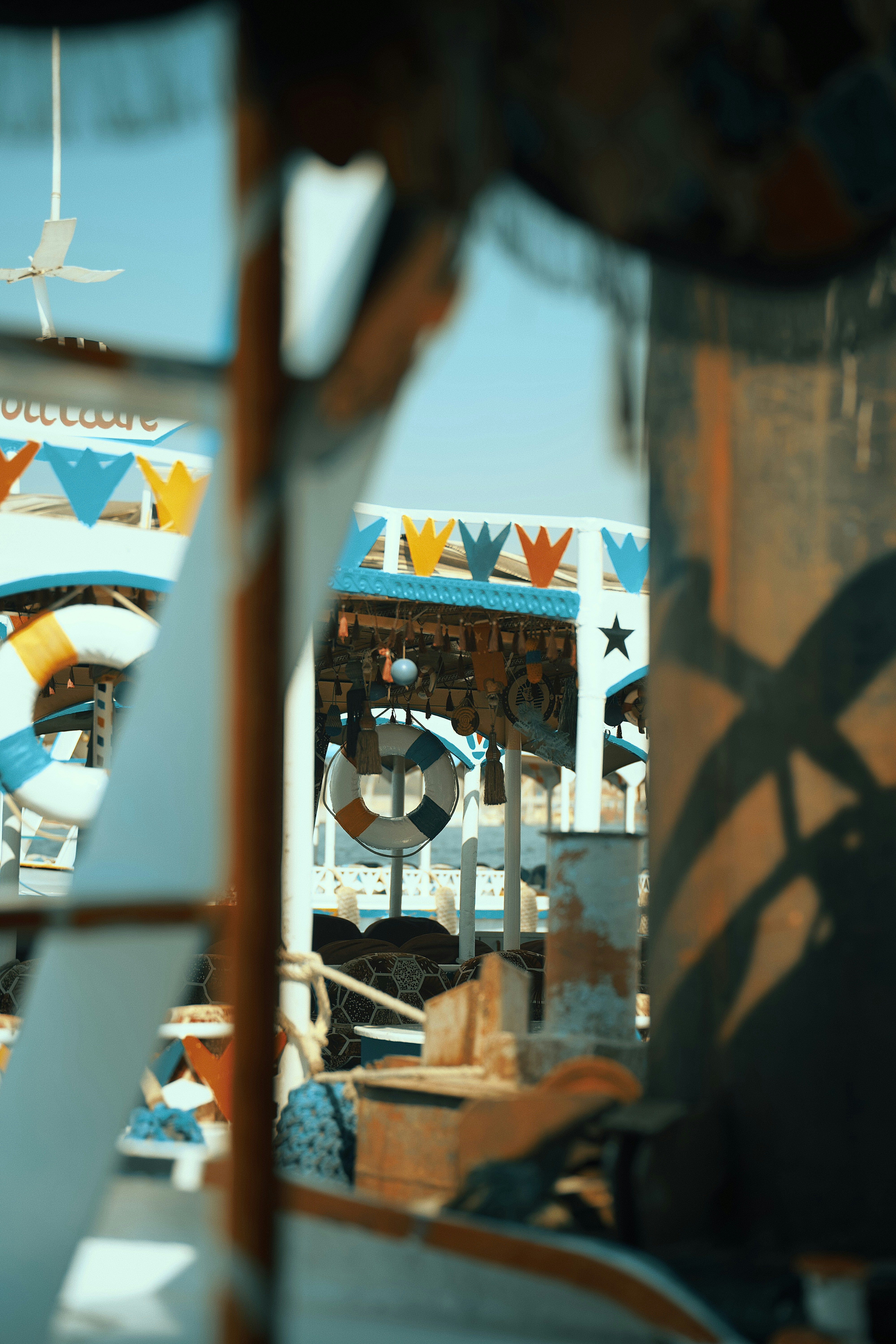 Vibrant marina scene captured through a narrow passage, with colorful pennants, lifebuoys and weathered structures visible in the background.
