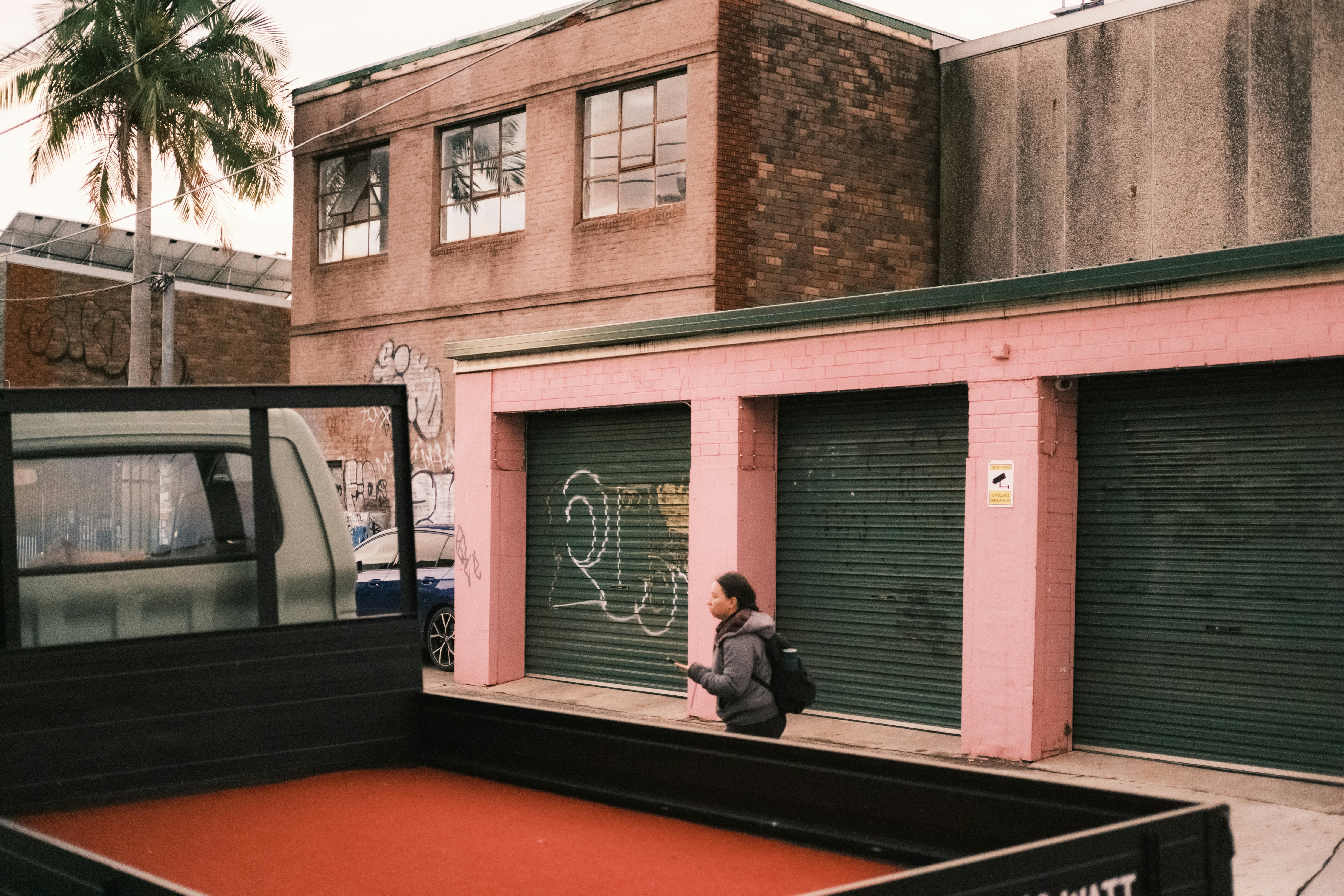 Sunlit storefronts and a lone passerby by the pink wall