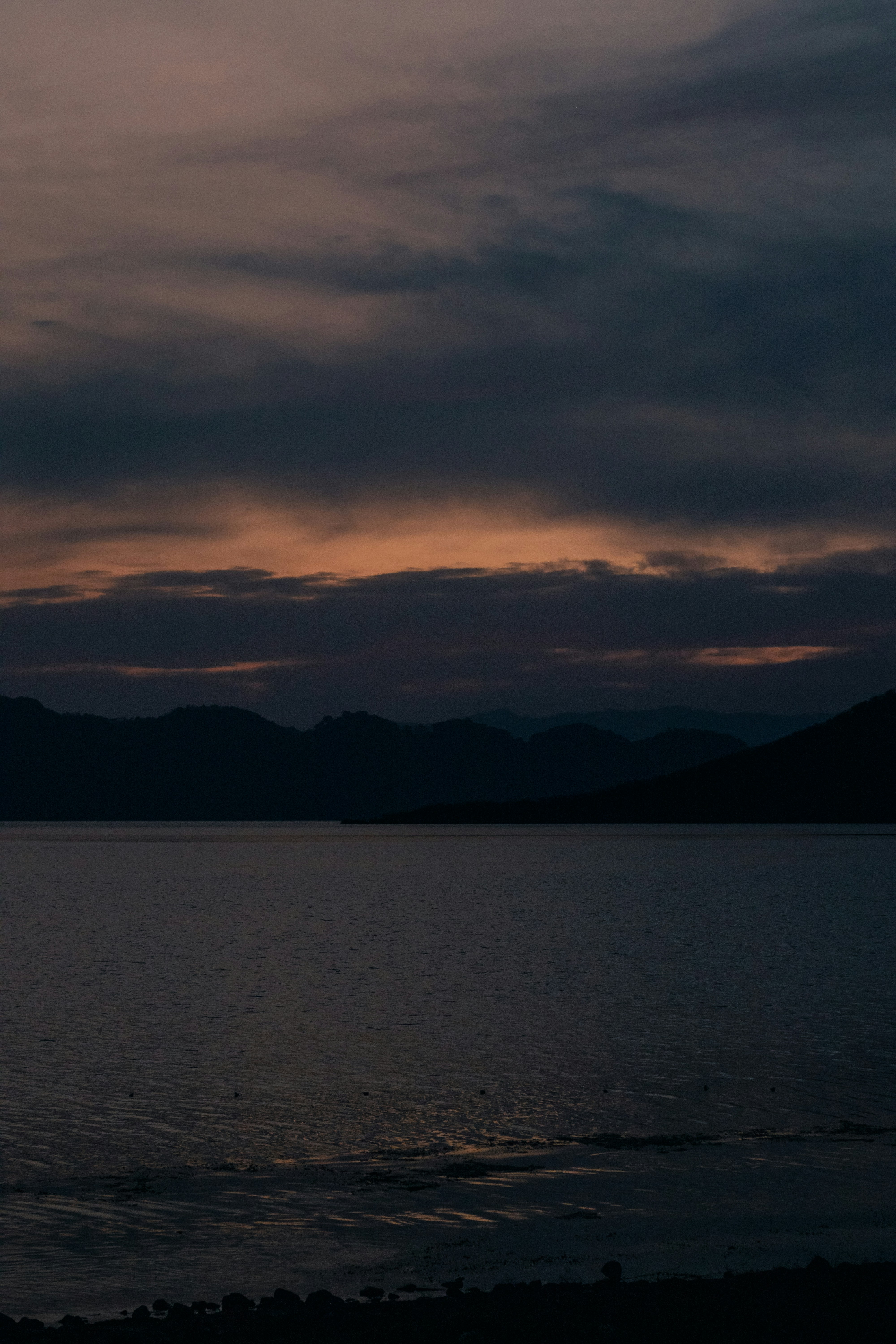 Dusk over Quiet Shore: A silhouette of distant hills against a moody, clouded sky