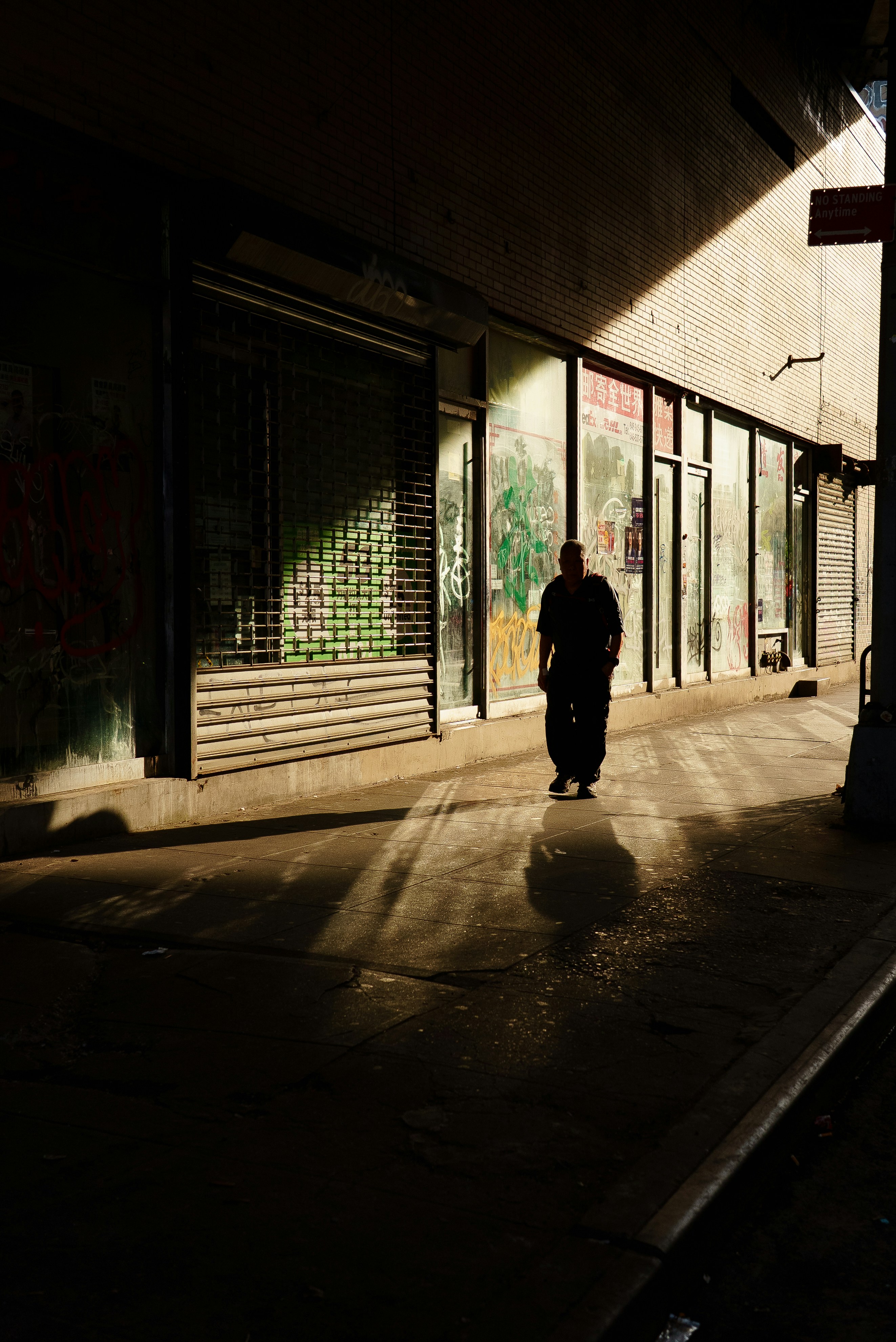 Shadowed Pedestrian in a Graffitied Alley Bathed in Narrow Beam
