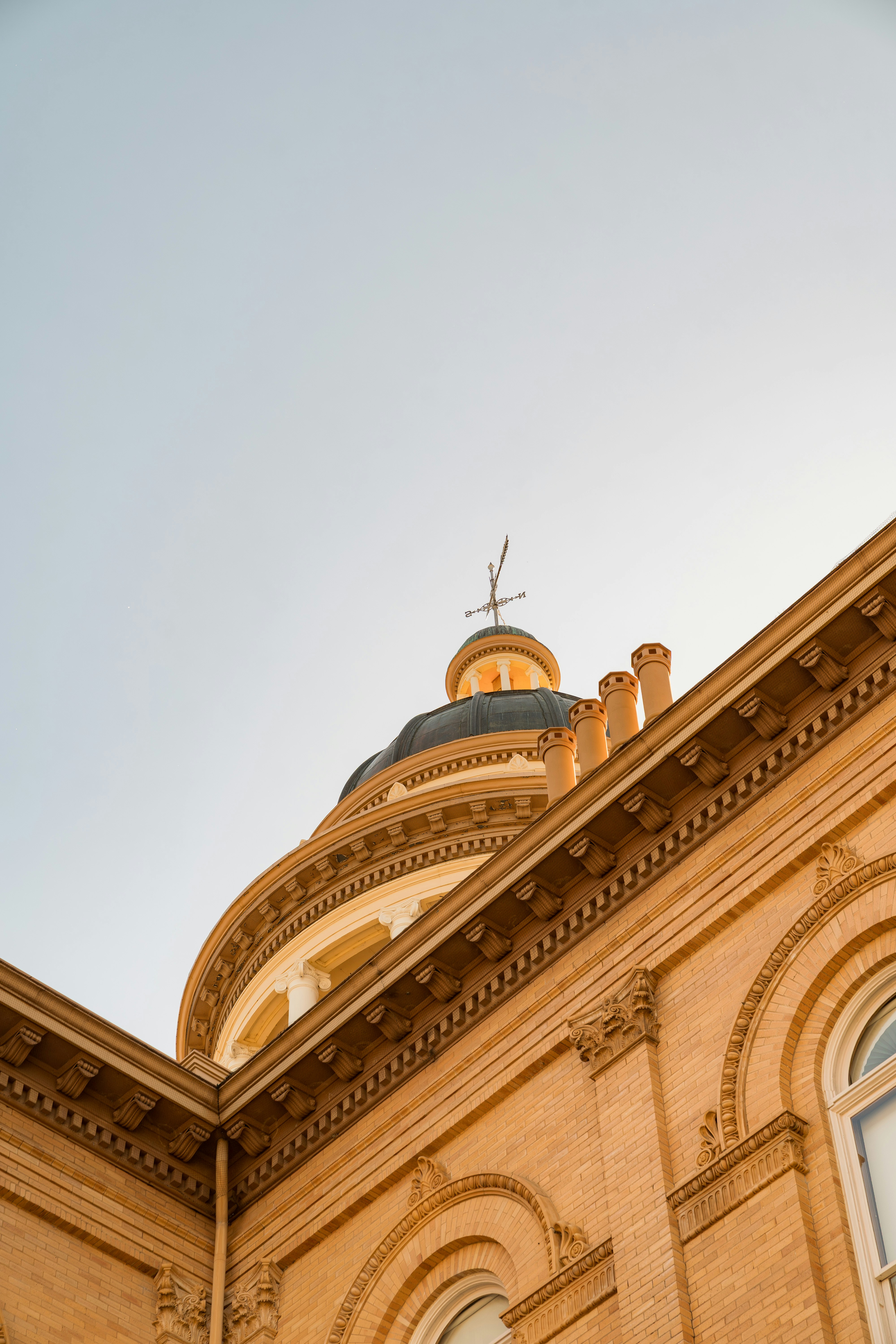 Amber-brick dome and ornate cornice rise against a clear sky, captured from an upward angle to emphasize architectural detail. A logo-like domed turret anchors the composition.
