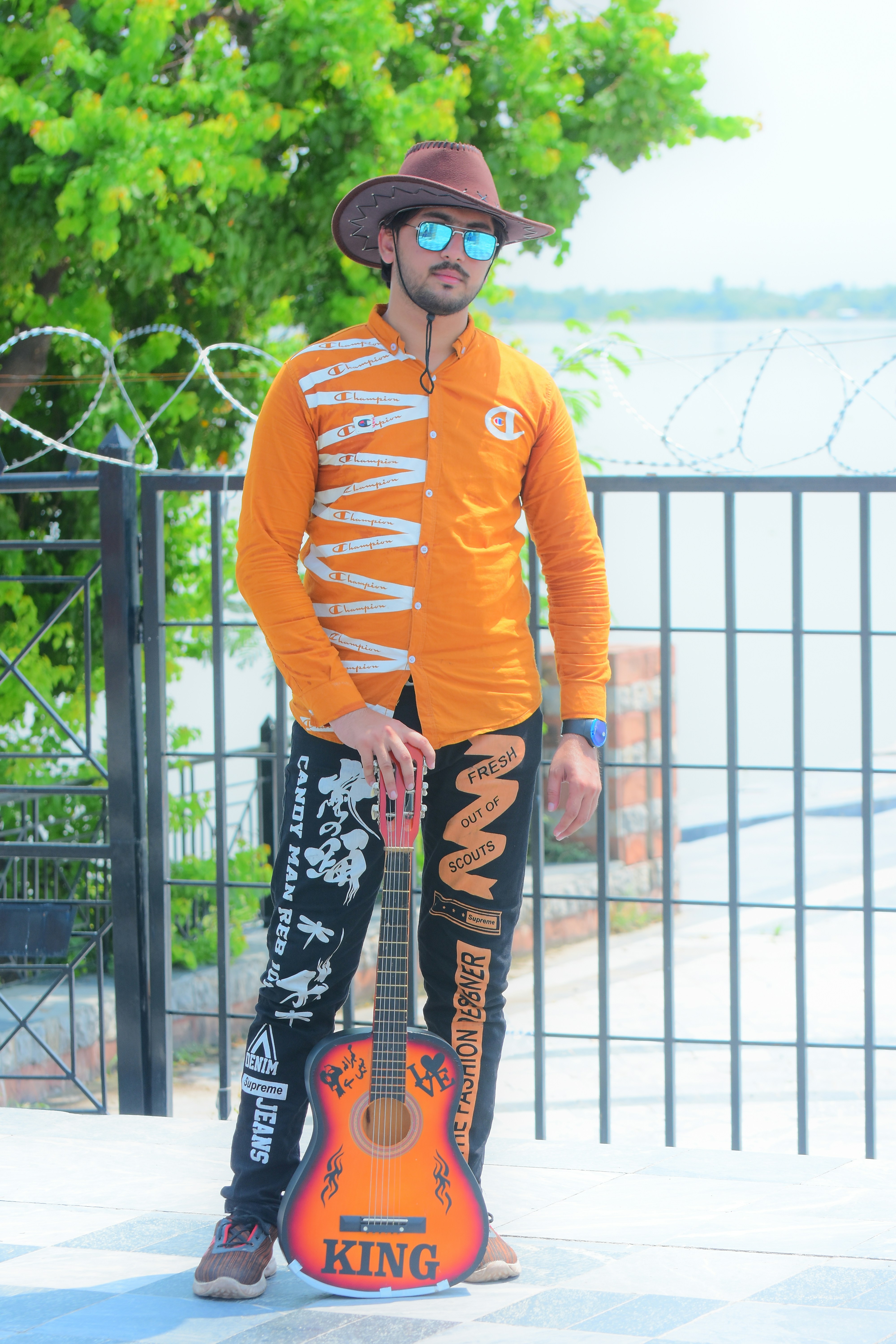 Sunlit Orange: A Guitar Hero Poses with a Bright Strat in Front of a Scenic Fence