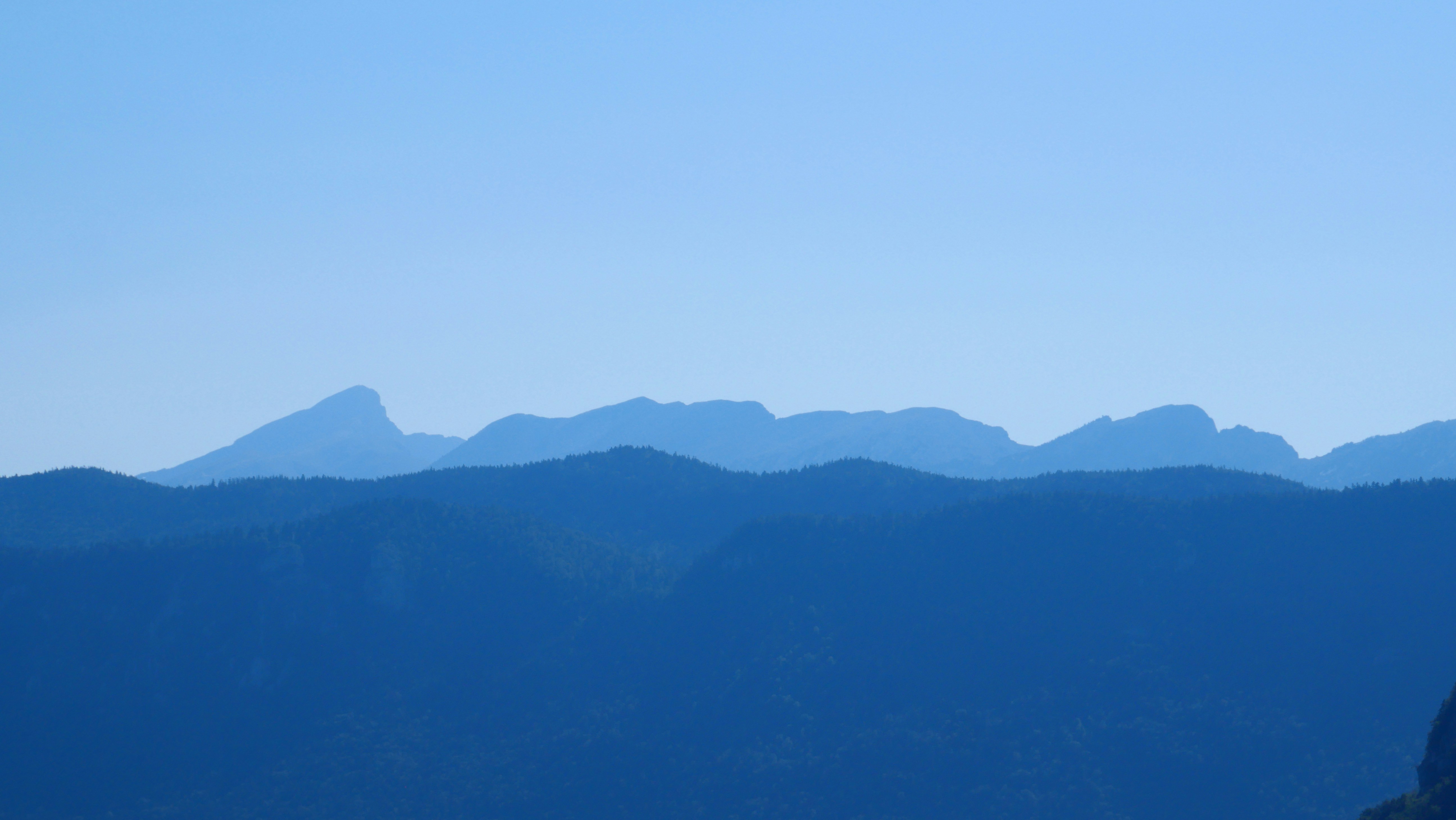 Blue ridge silhouette stretches across the horizon under clear sky, emphasizing layered mountain peaks in cool tones. A landscape scene capturing distant ranges and tranquil atmosphere.