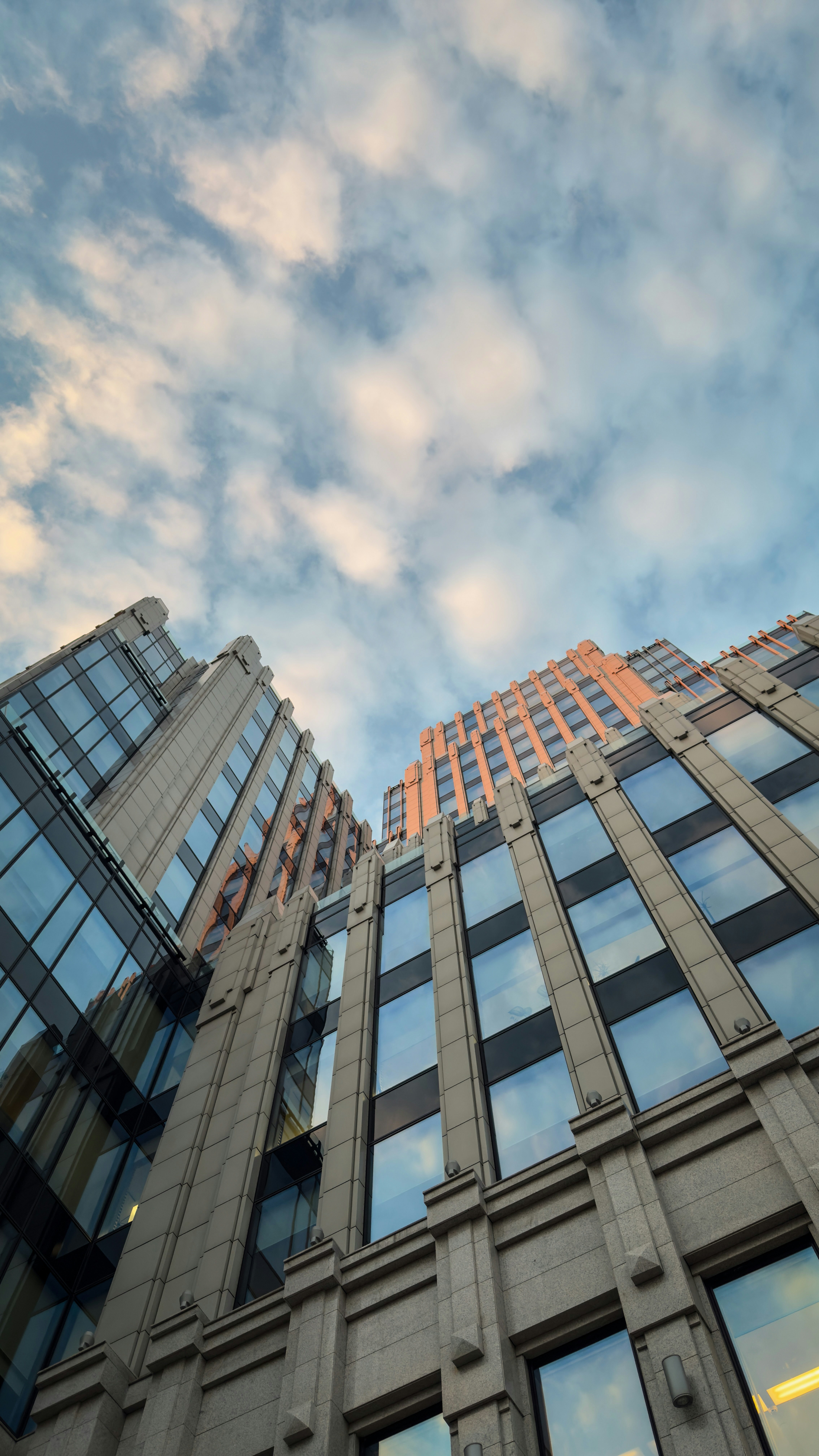 Modern glass-and-stone building towers into a pale sky, capturing the converging lines and reflective panels as daylight softens the edges.