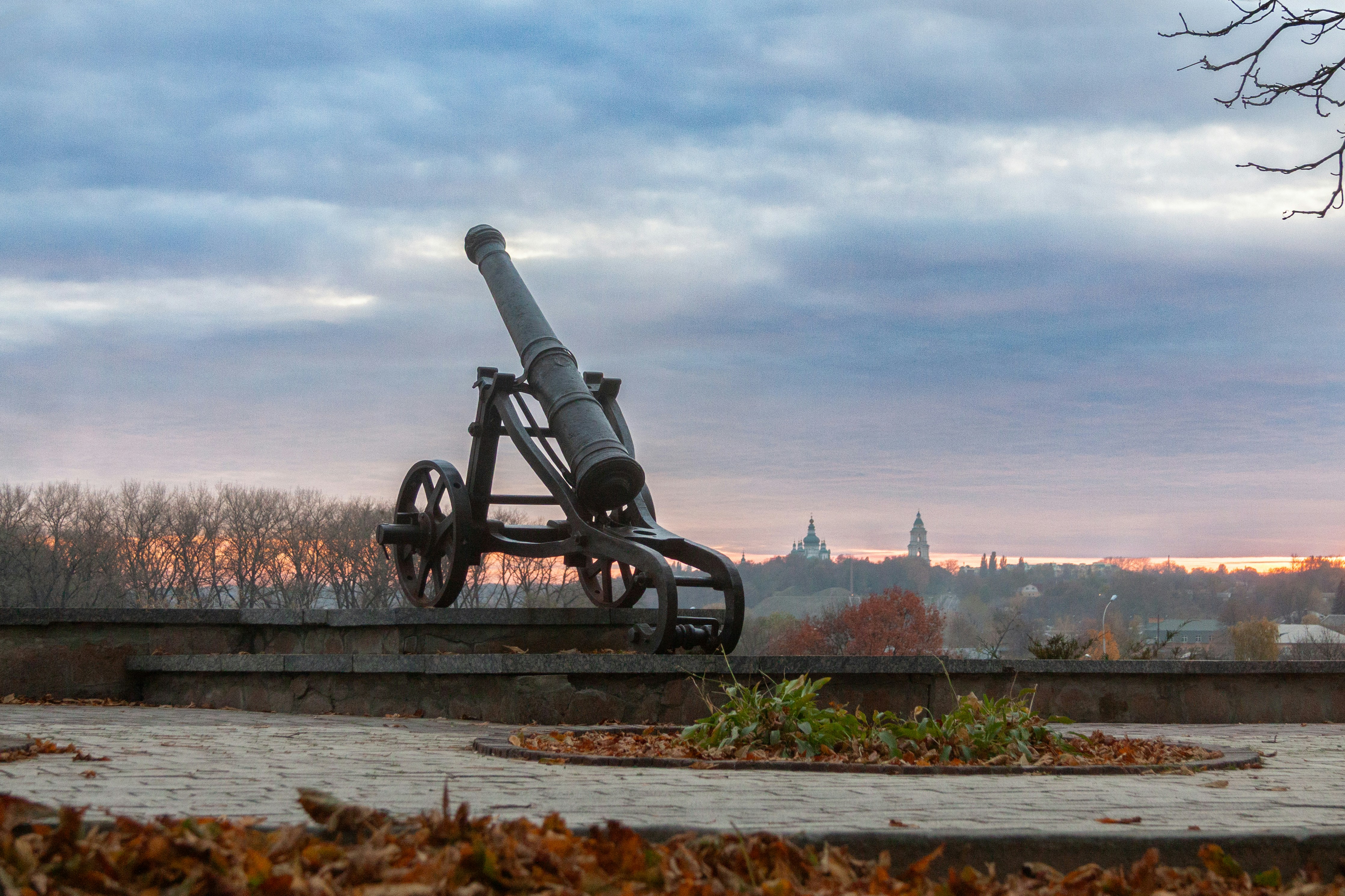 Low-angle shot of an old cannon on a stone platform with a soft sunset and distant skyline; a calm, atmospheric scene emphasizing history and landscape.