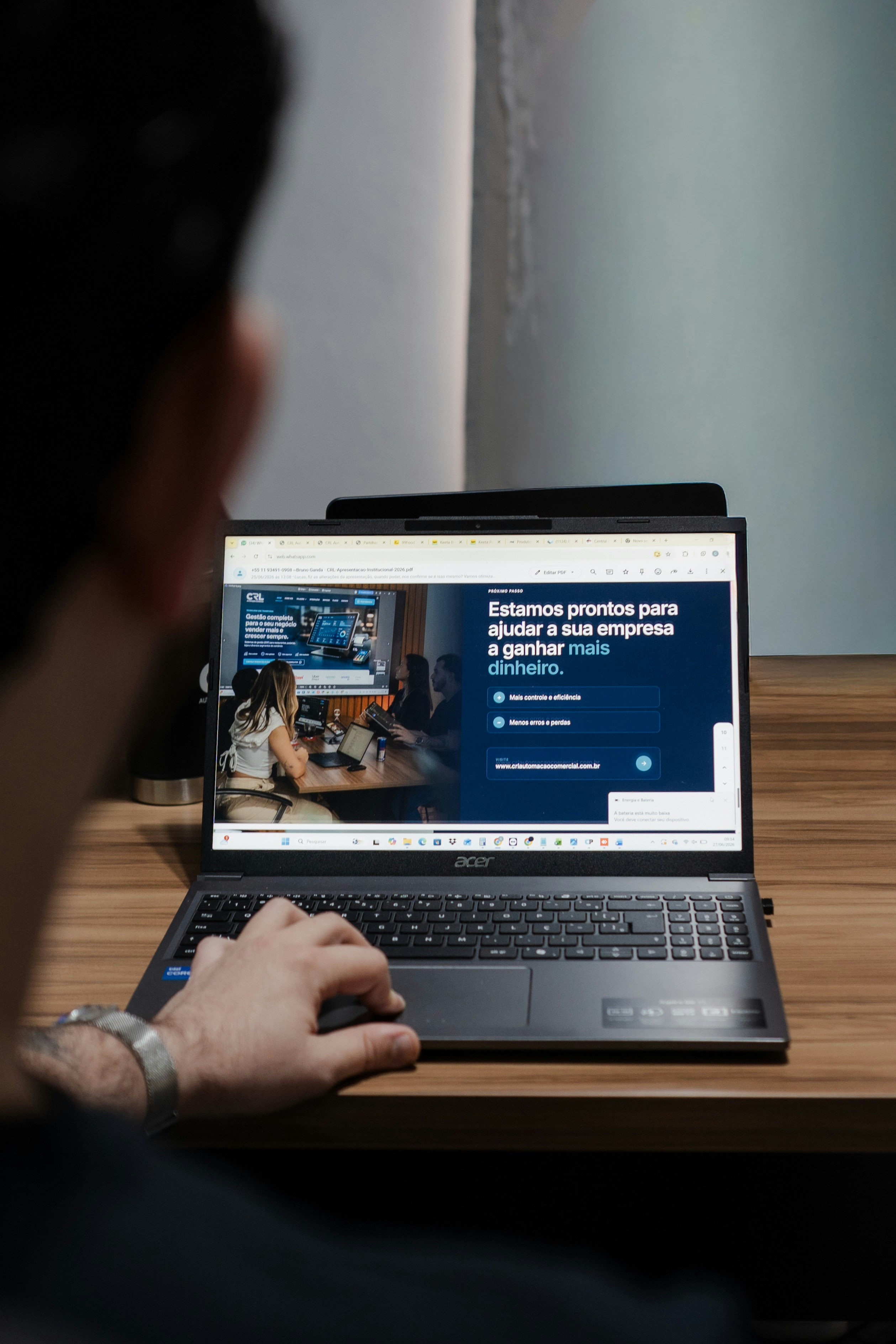 Close-up view of a person using a laptop on a wooden desk, screen showing a business webpage; minimal background and shallow depth reveal a work environment.