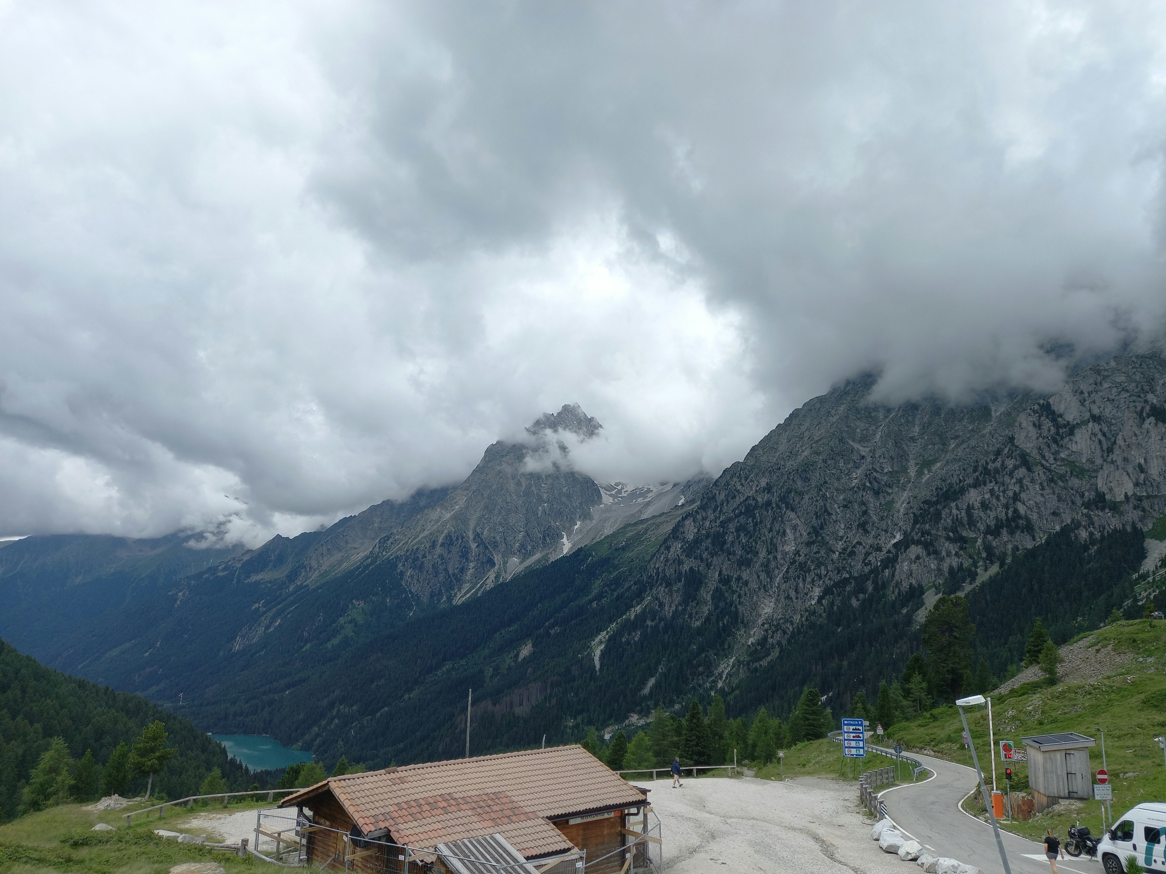 A winding mountain road threads through a small alpine settlement beneath looming, cloud-clad peaks.