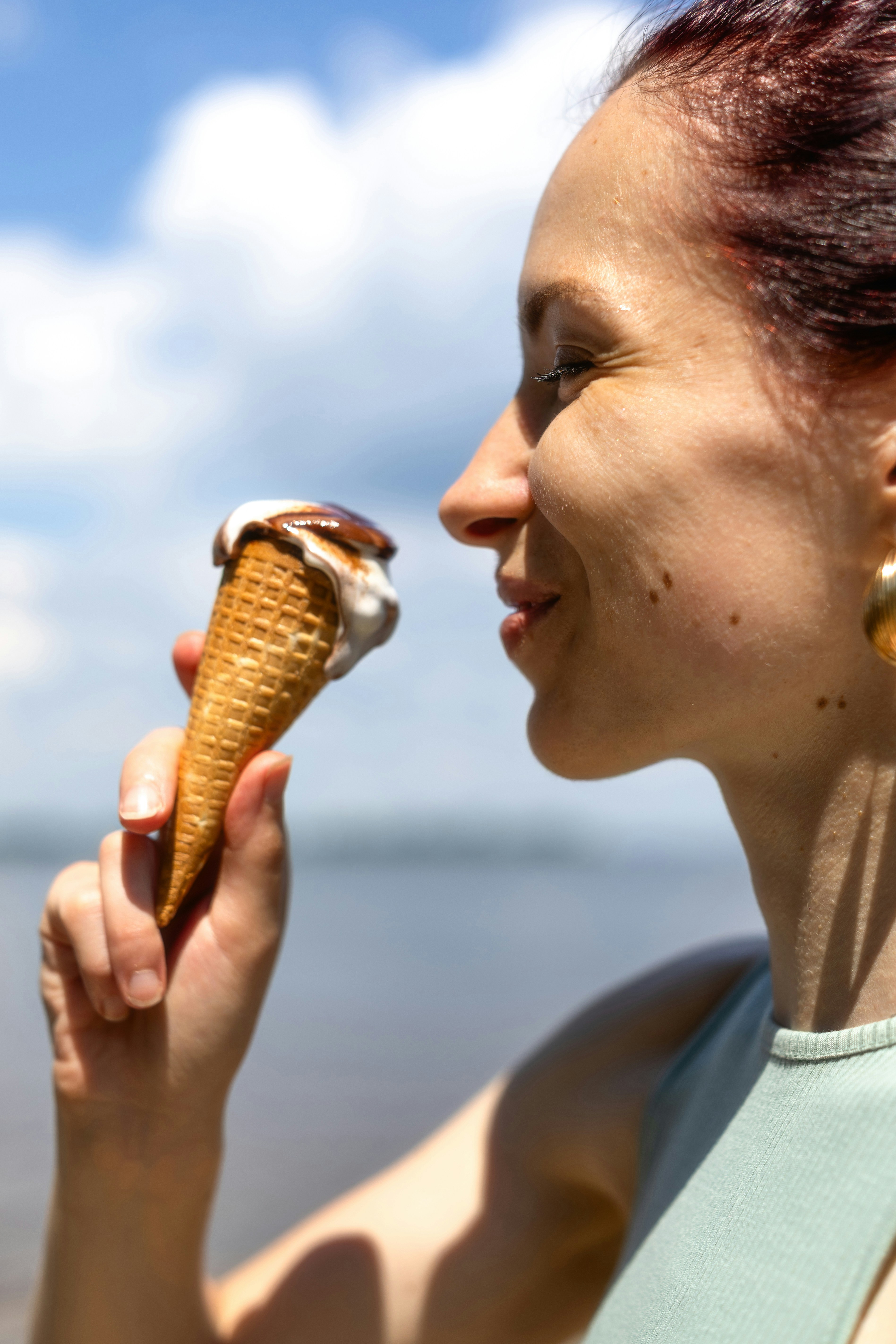 A Sunlit Bite: Close Portrait of a Woman Enjoying an Ice Cream Cone by the Sea