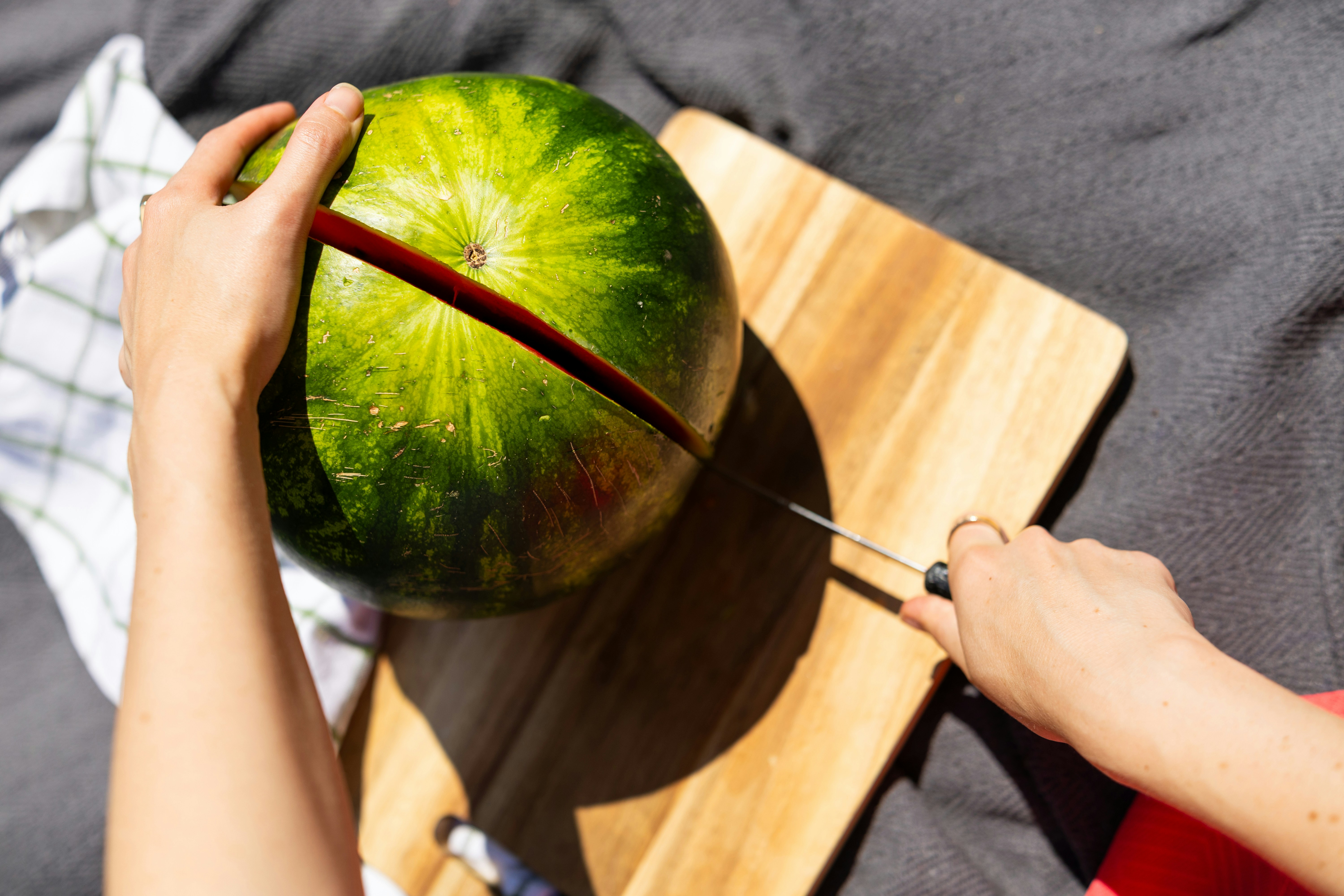Hand-Carved Slice: A Knife Delves into a Watermelon on a Wooden Board