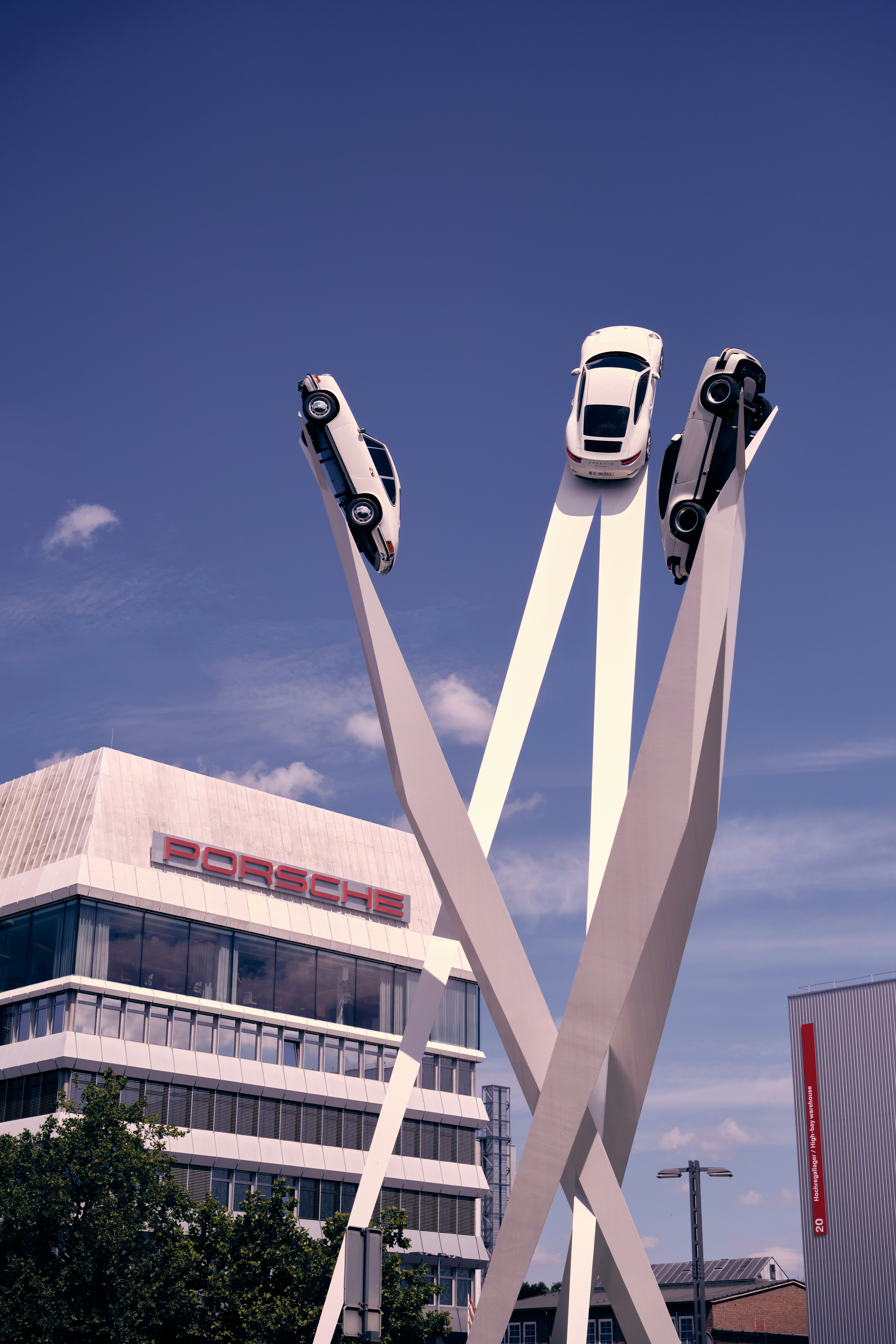 Rising Monuments: Cars perched on sculptural beams against a Porsche backdrop