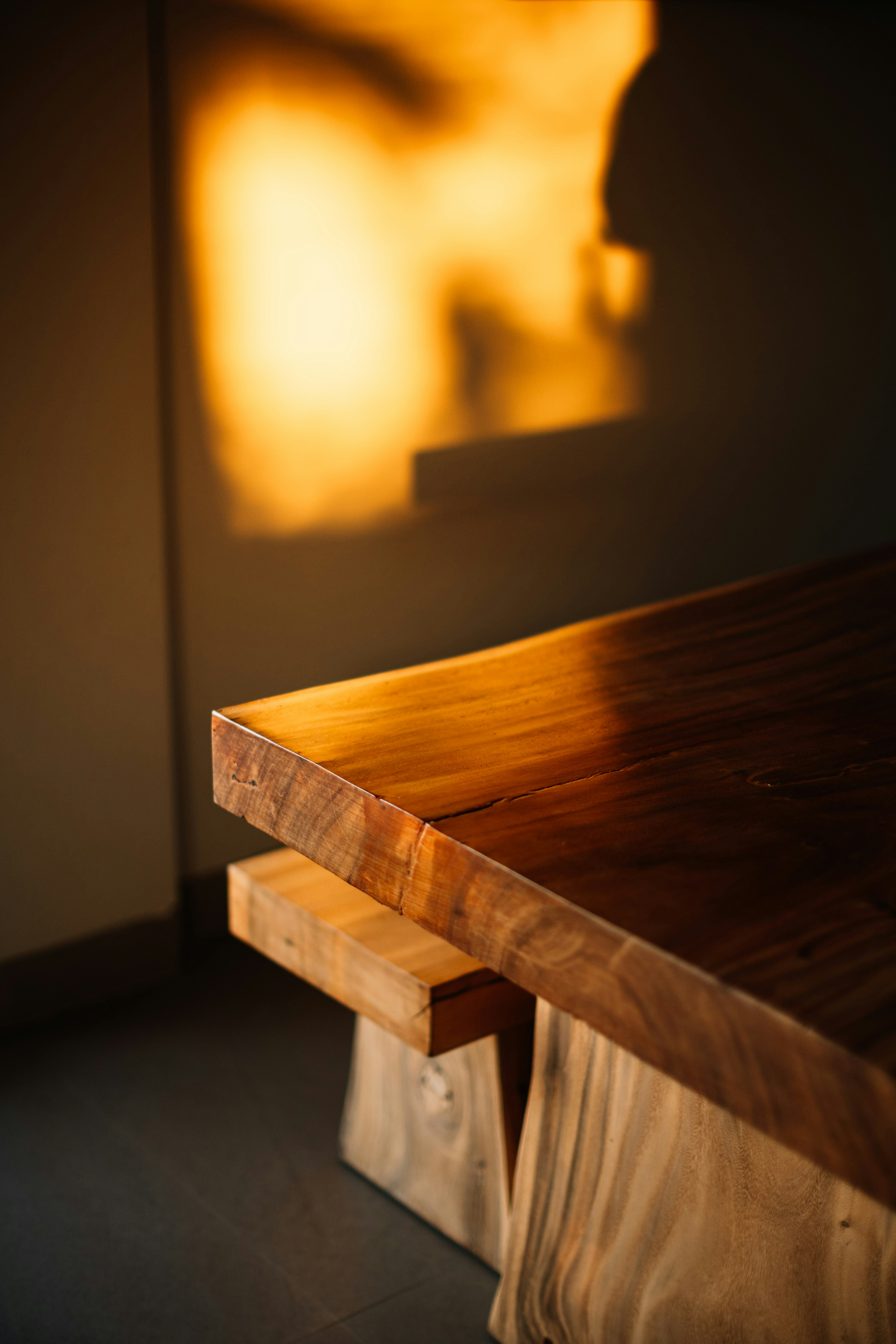 Warm wall glow and a sunlit wooden table edge in soft focus, emphasizing texture and craft. The scene conveys a quiet, intimate interior with a focus on the table’s grain; no people or logos present.