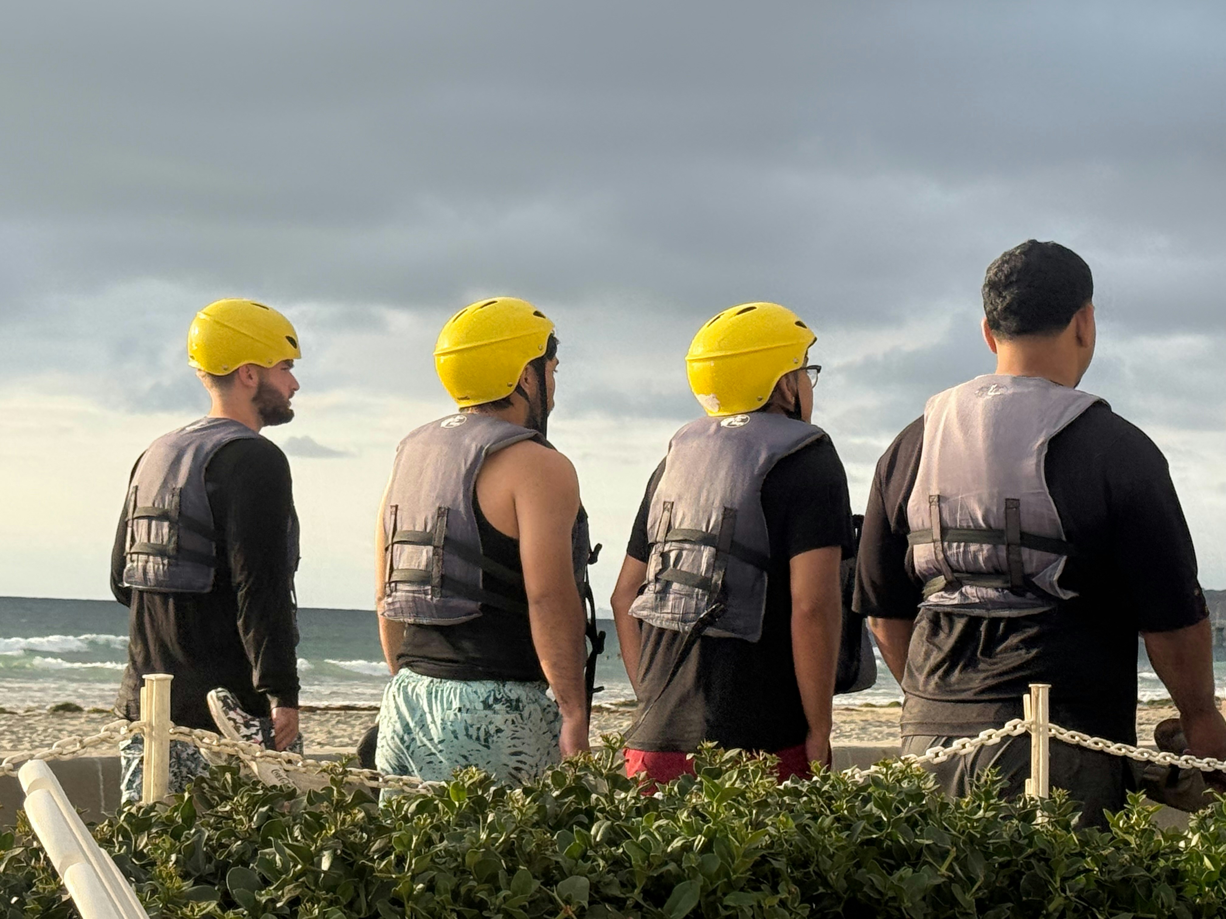 Men in helmets and life vests on a beach.