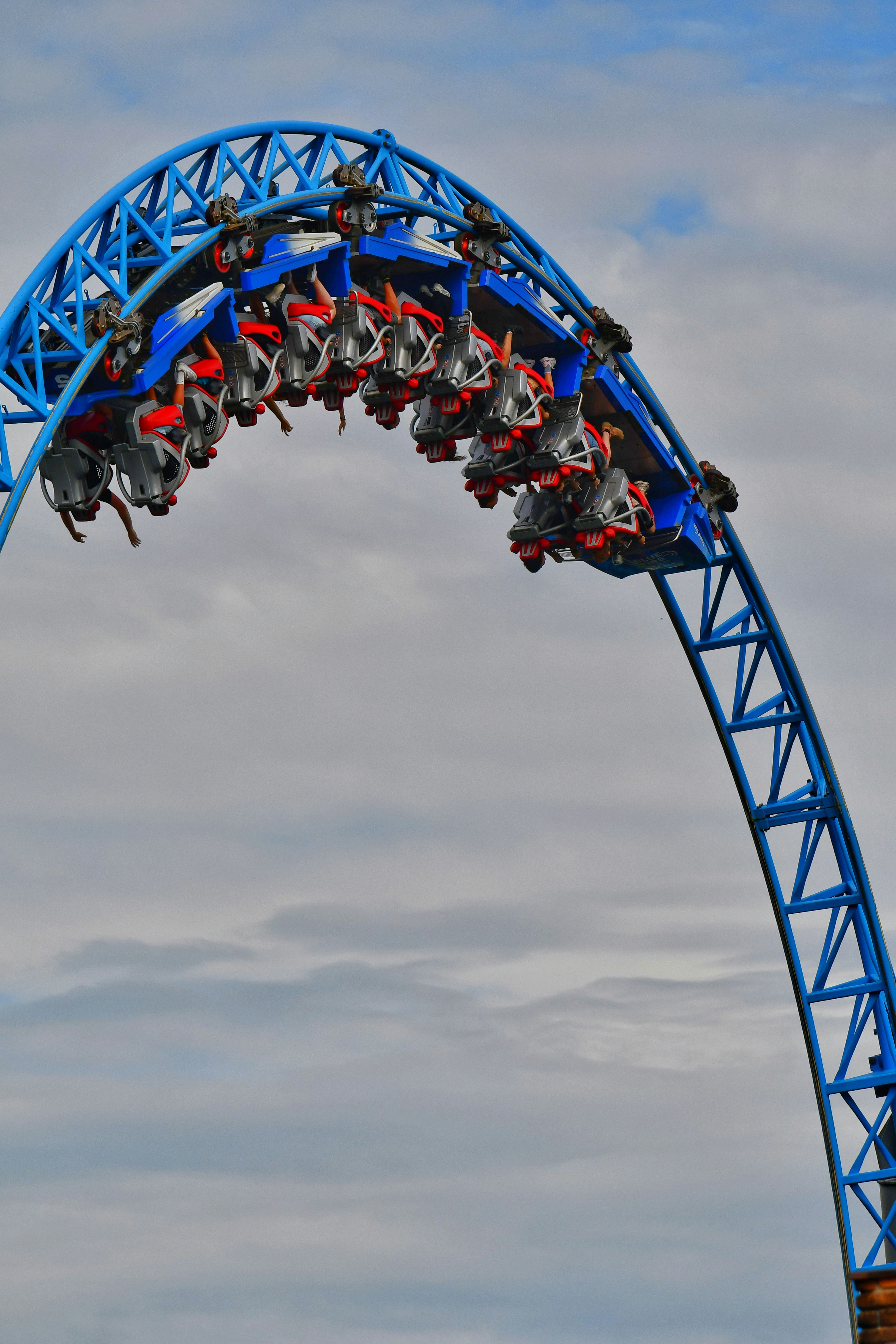 Thrilling blue roller coaster loop with riders inverted against sky.