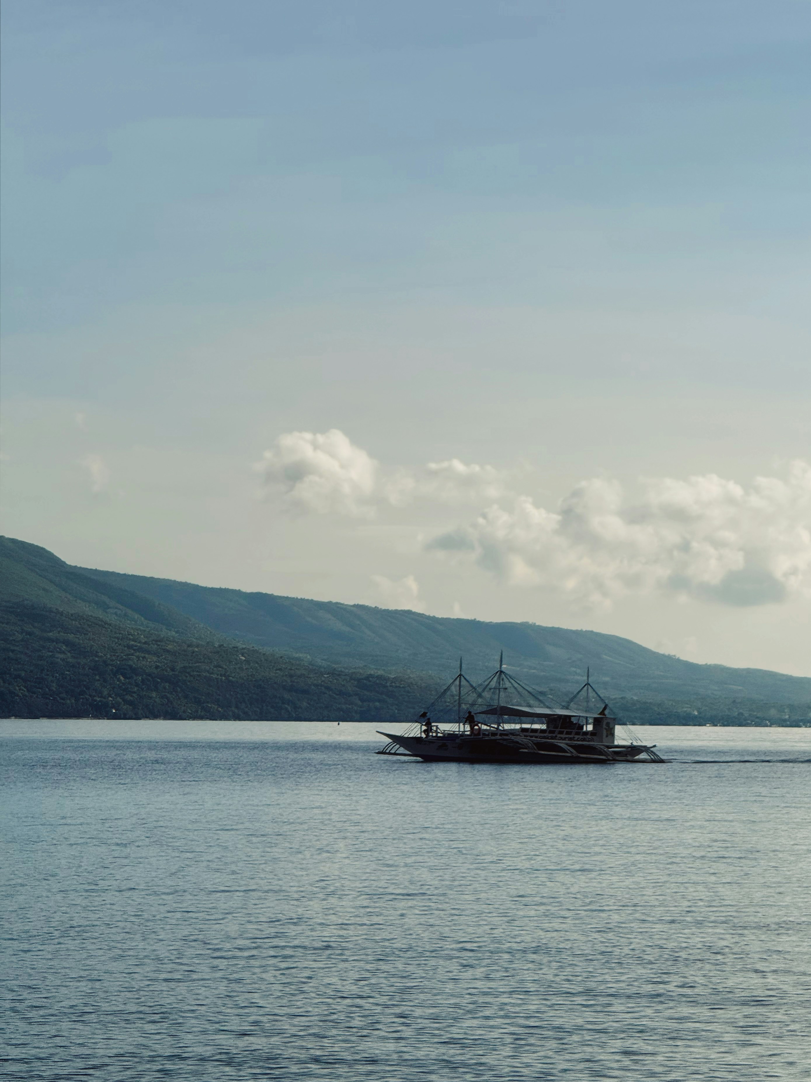 Calm lake with a lone boat near the horizon, framed by distant hills and a soft, cloudy sky.