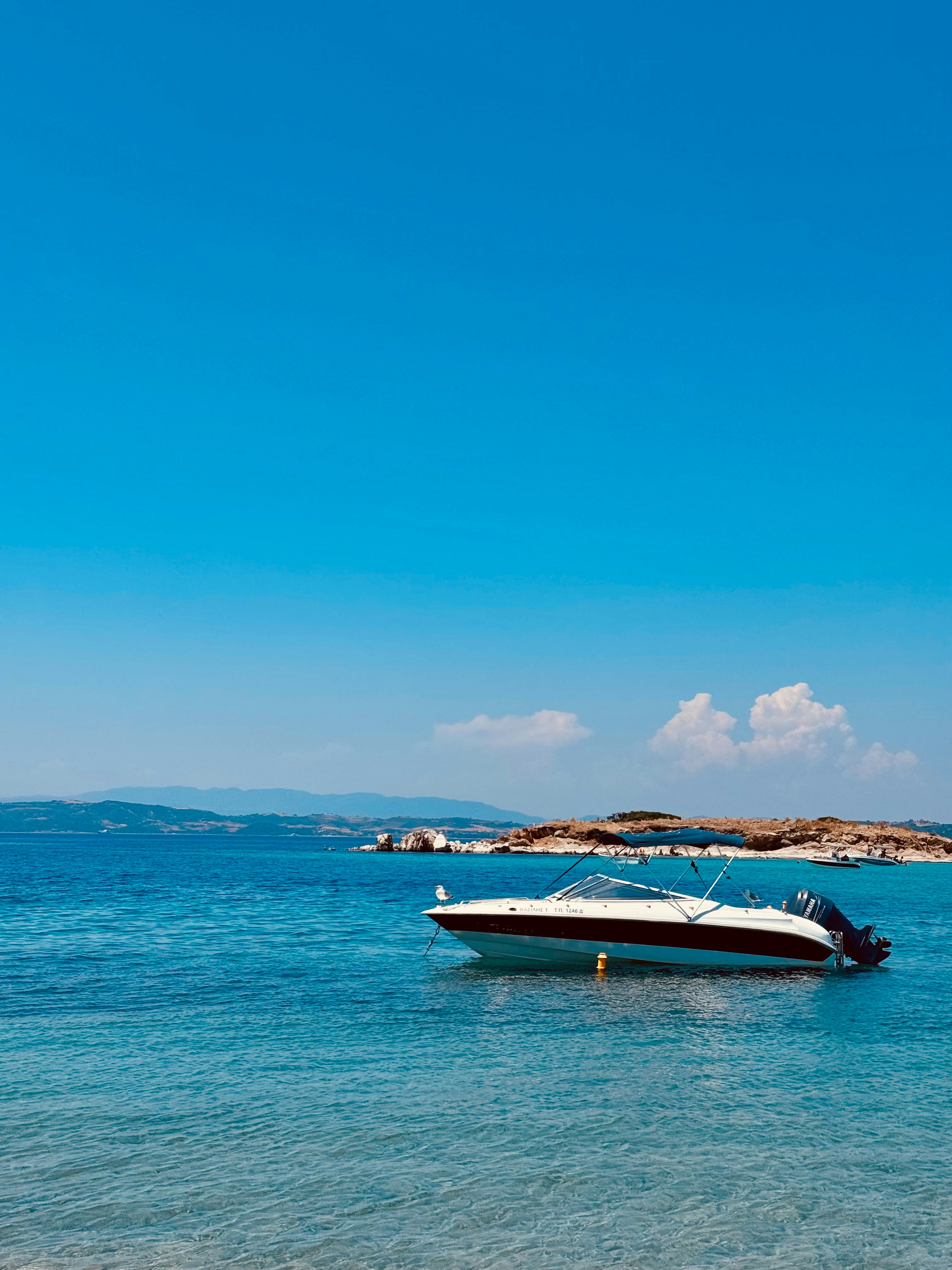 Sunlit Sea: A lone speedboat at anchor near rocky shore