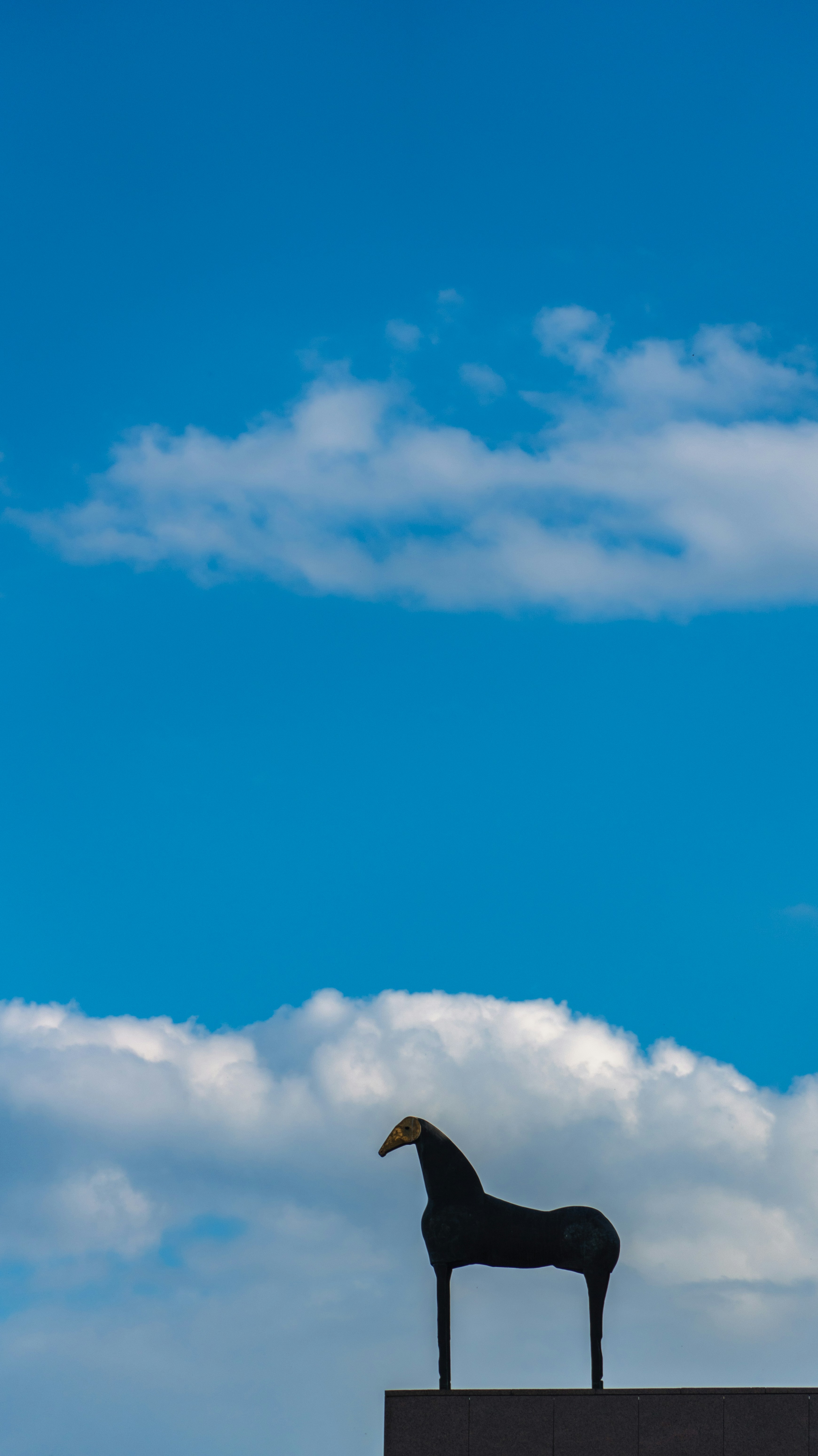 Silhouette on the Skyline: A lone horse-like sculpture anchors the building beneath a bright blue sky