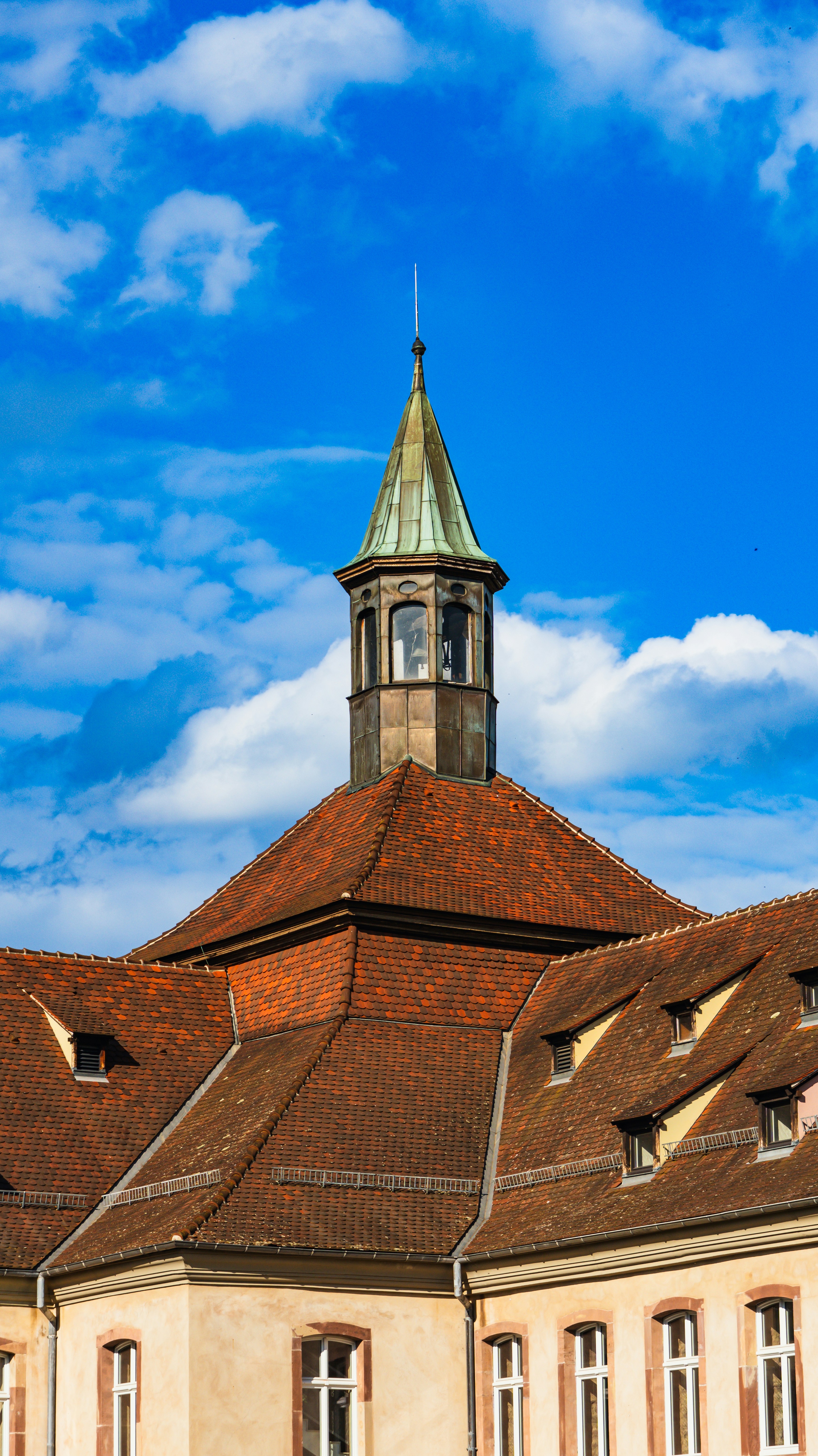 Brick-roofed building with a tall, copper-green spire rising against a blue sky; architectural details and windows line the lower facade. This is a photograph of a historical house with a clocktower-like tower.