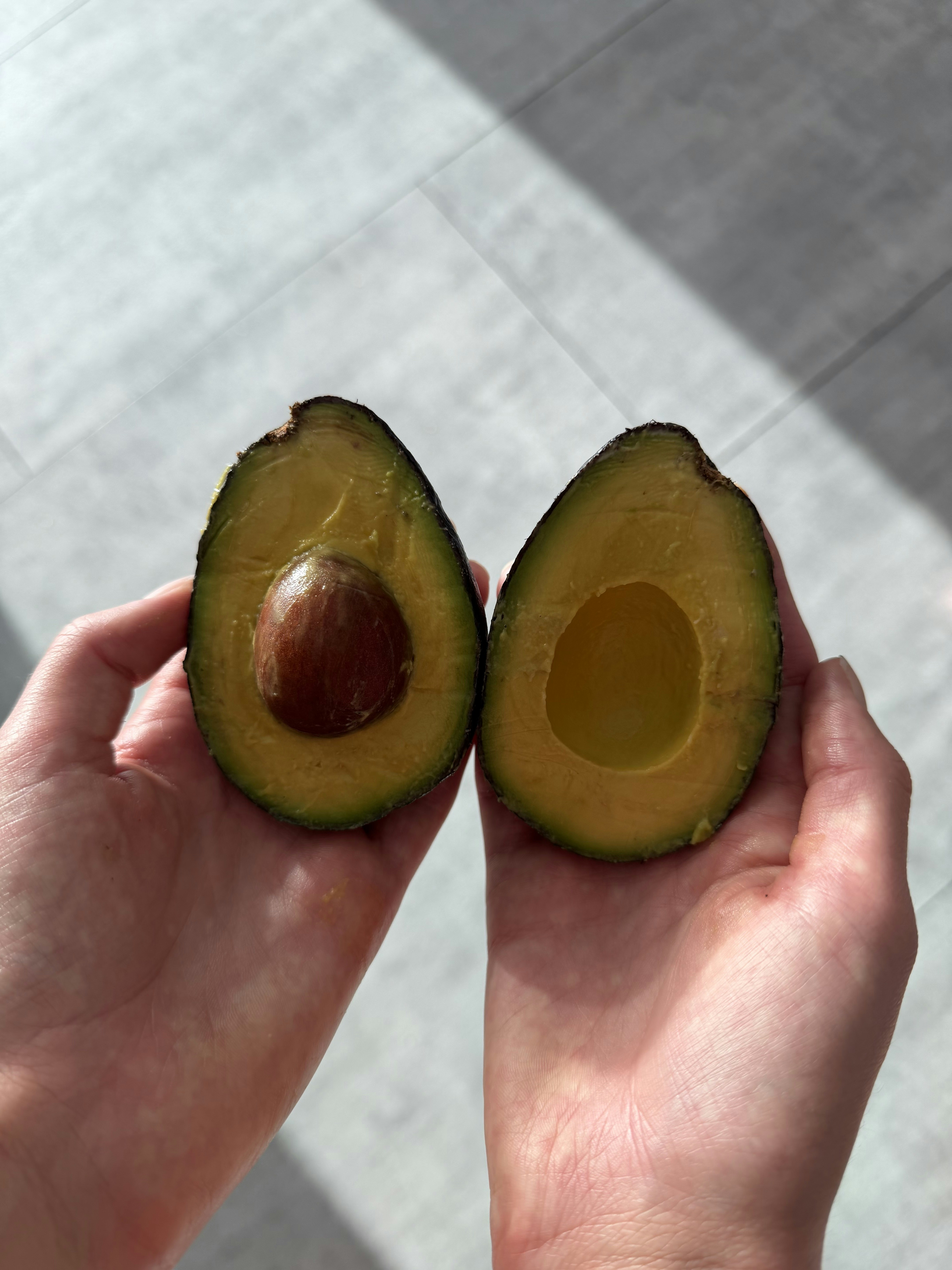 Split Avocado: Halved Fruit Gripped by Hands in Sunlit Outdoor Surface