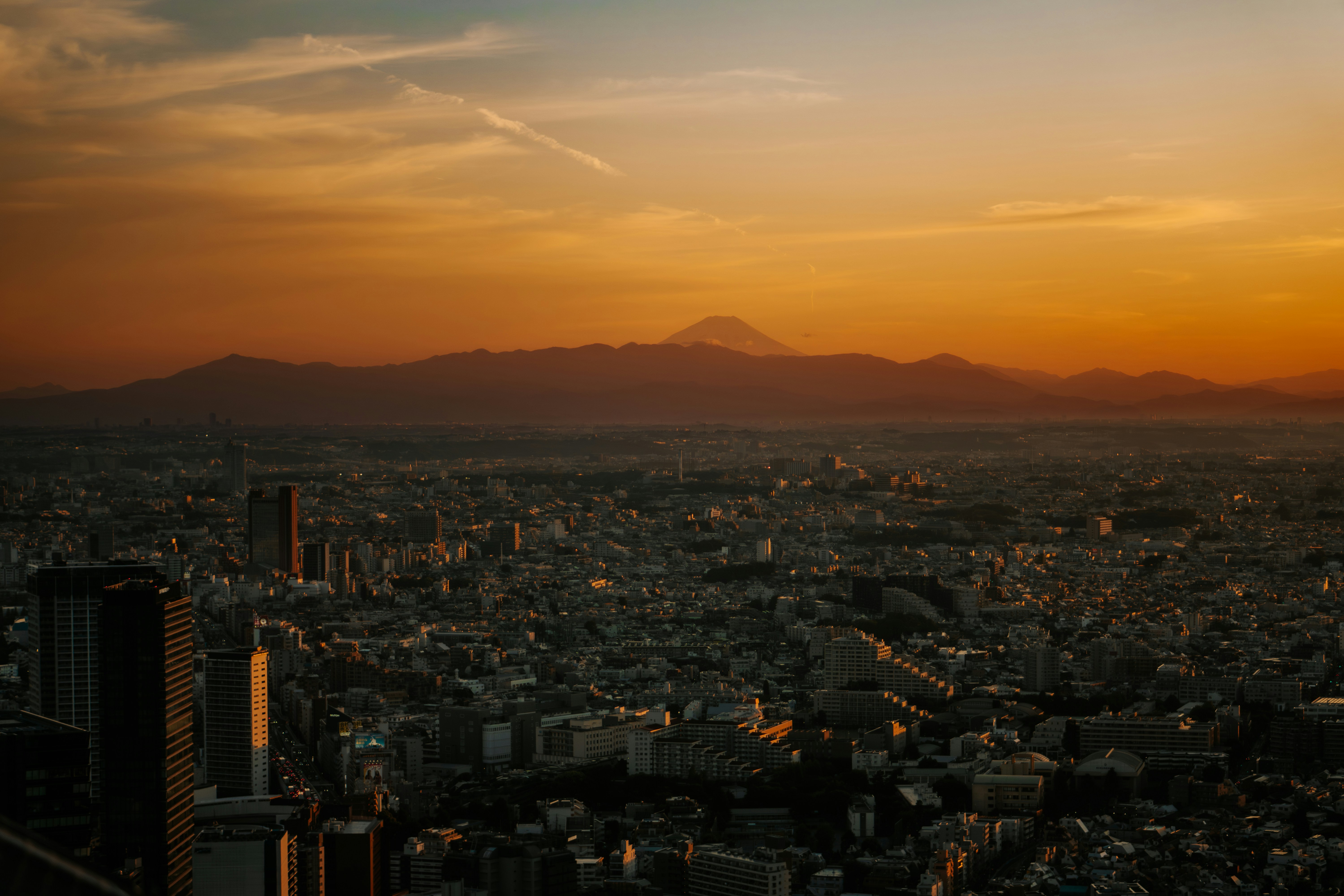 Sunset Over the Urban Sea: Distant Volcano Silhouette Behind a Densely Packed Skyline