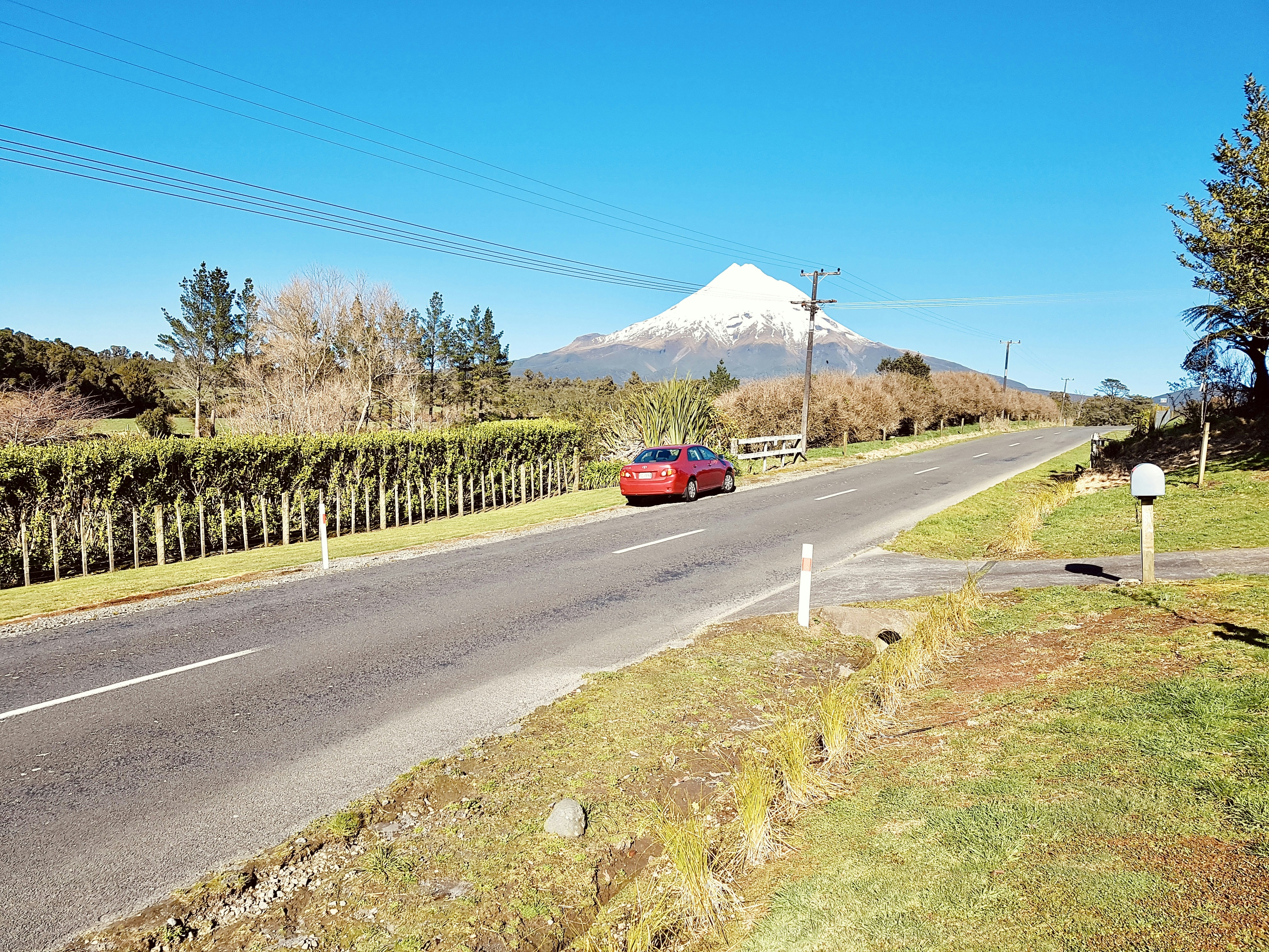 Red Car on a Quiet Rural Road with Snow-Capped Peak Behind