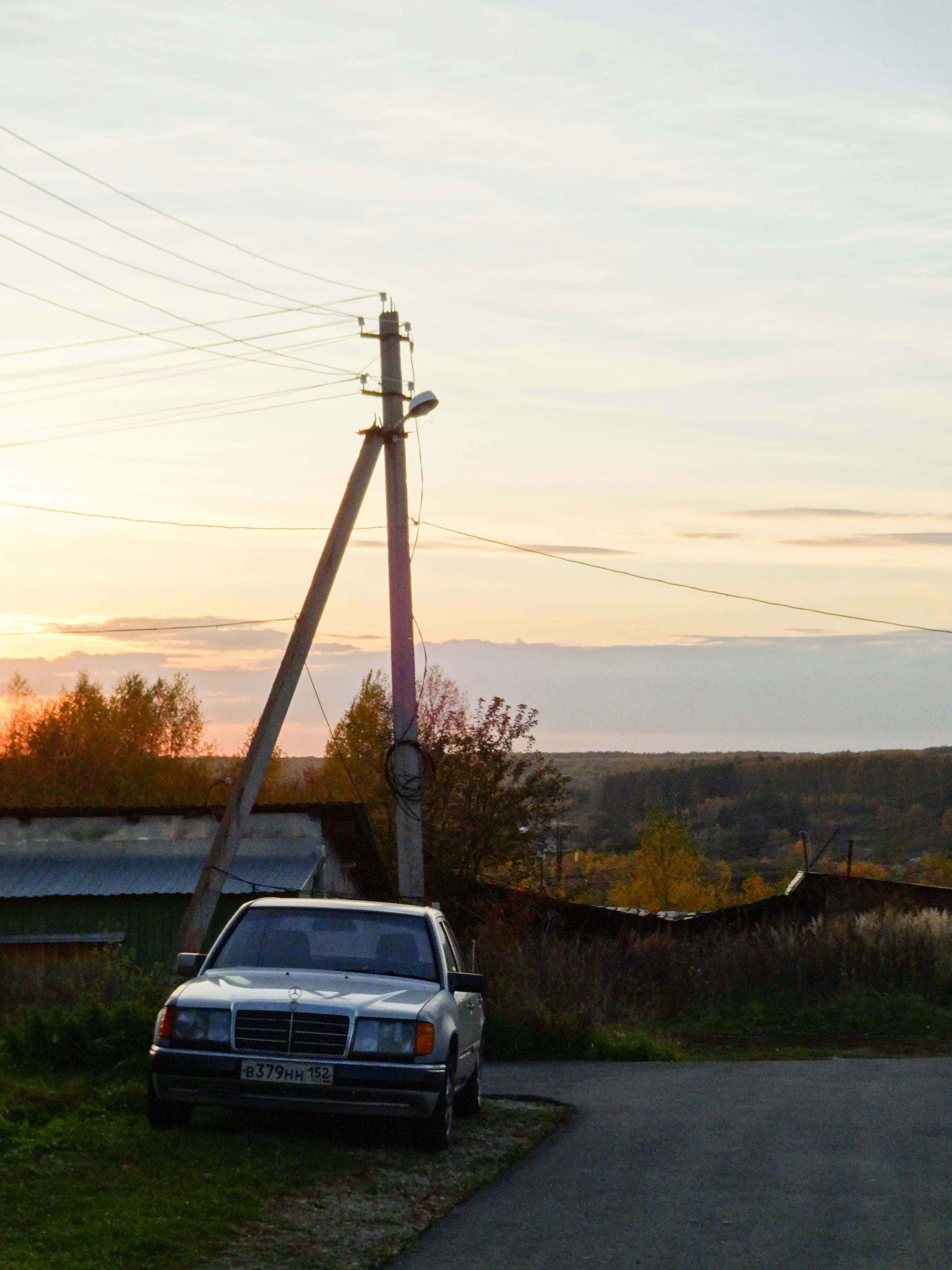 Sunset Quiet: A Silver Teal Car and Slanted Pole Beside a Winding Road