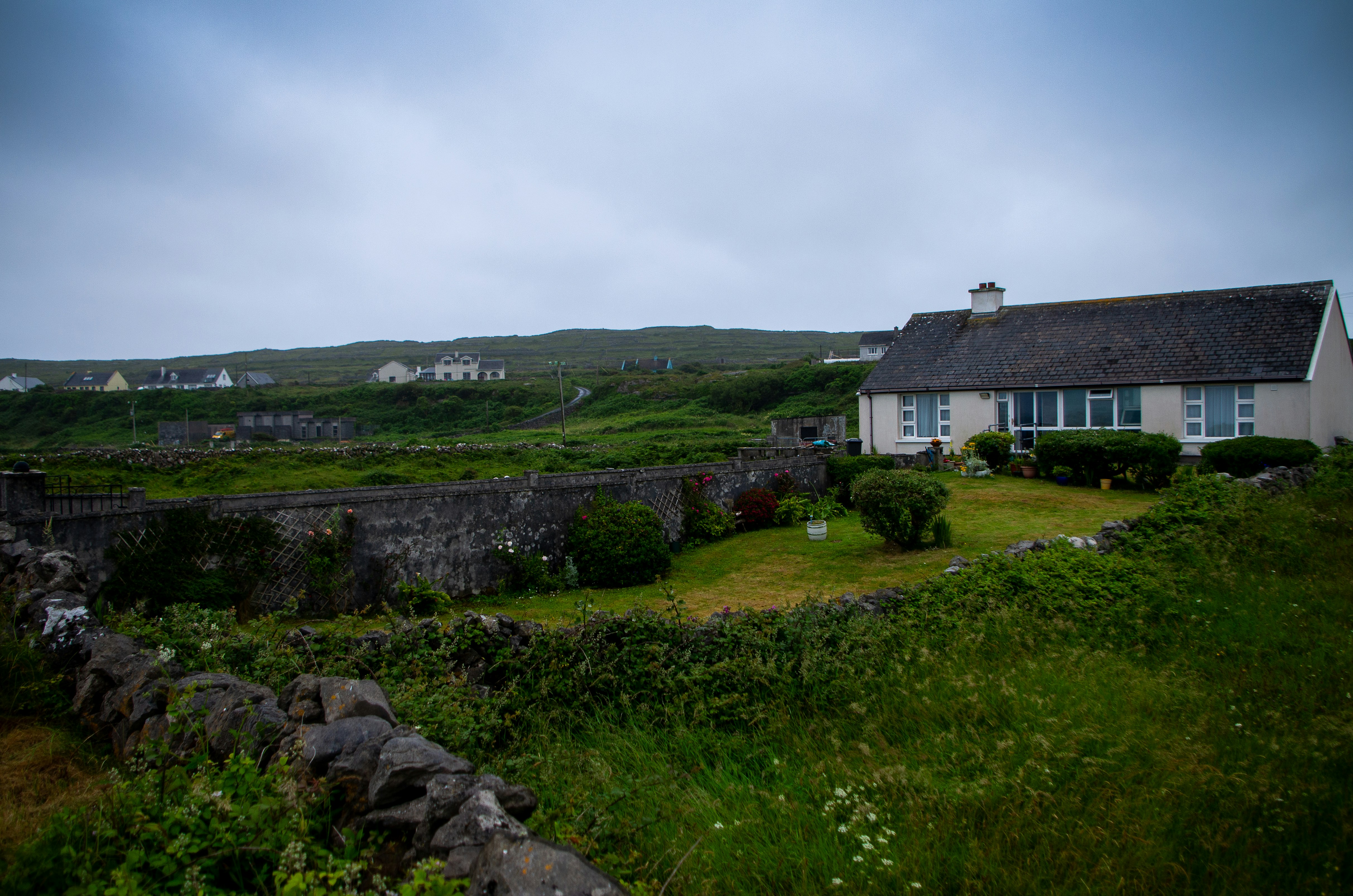 Cottage by the Stone Wall: Green Pastures under a Cloudy Sky