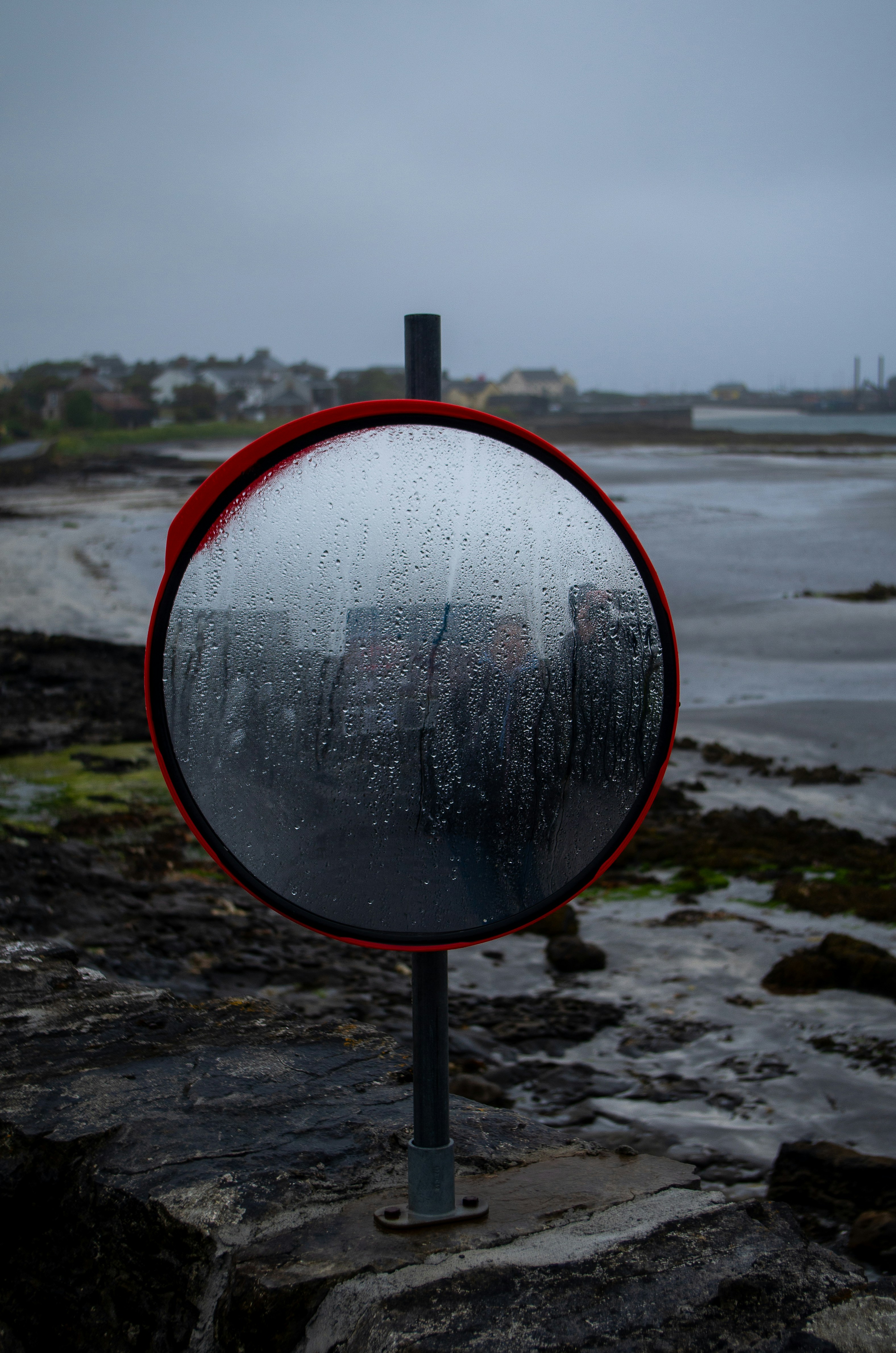 Circular Mirror in Rain: A Red Rim Reflecting a Diffuse Coastal Town