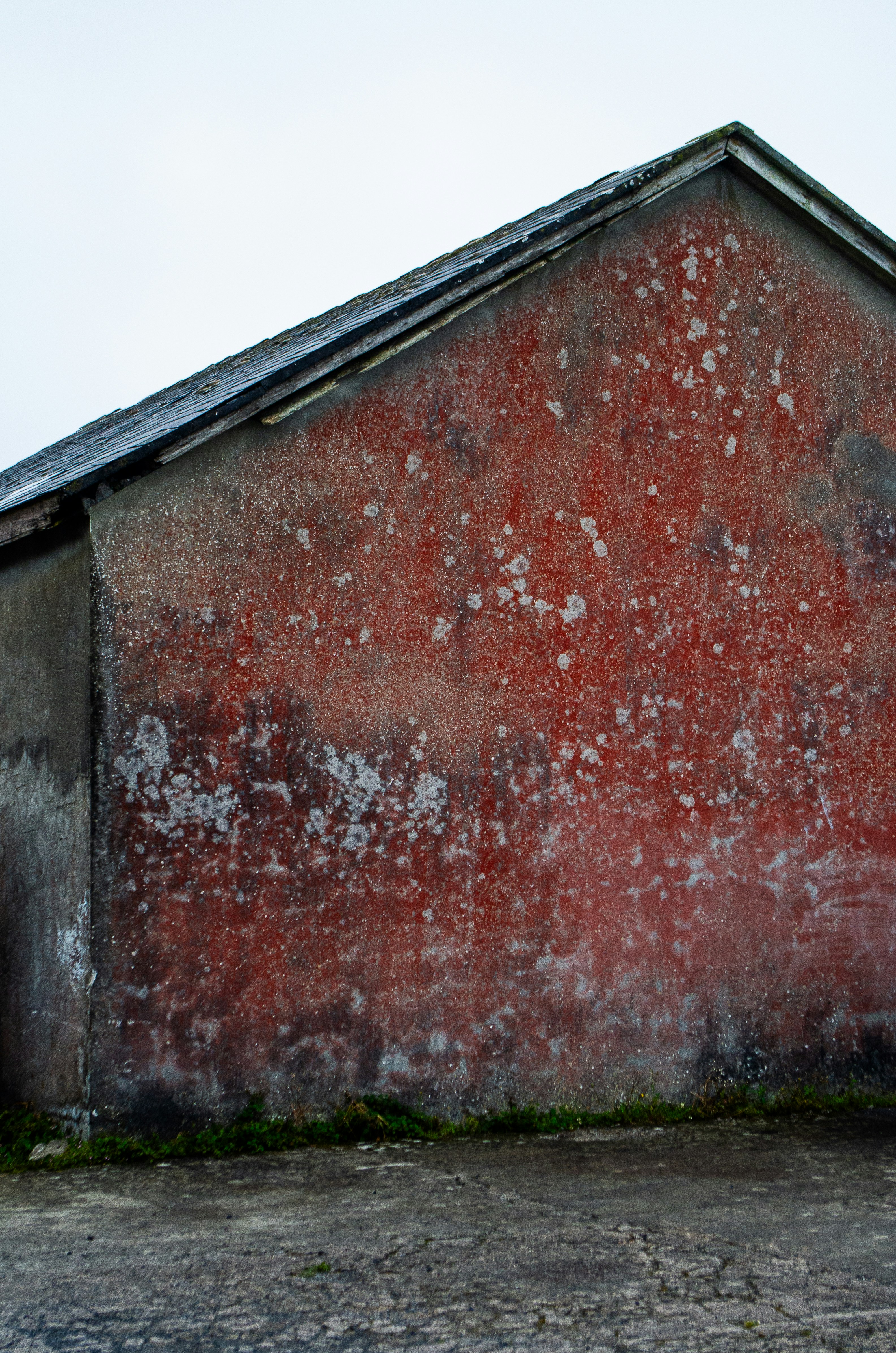 A weathered red building wall with white and grey patches.