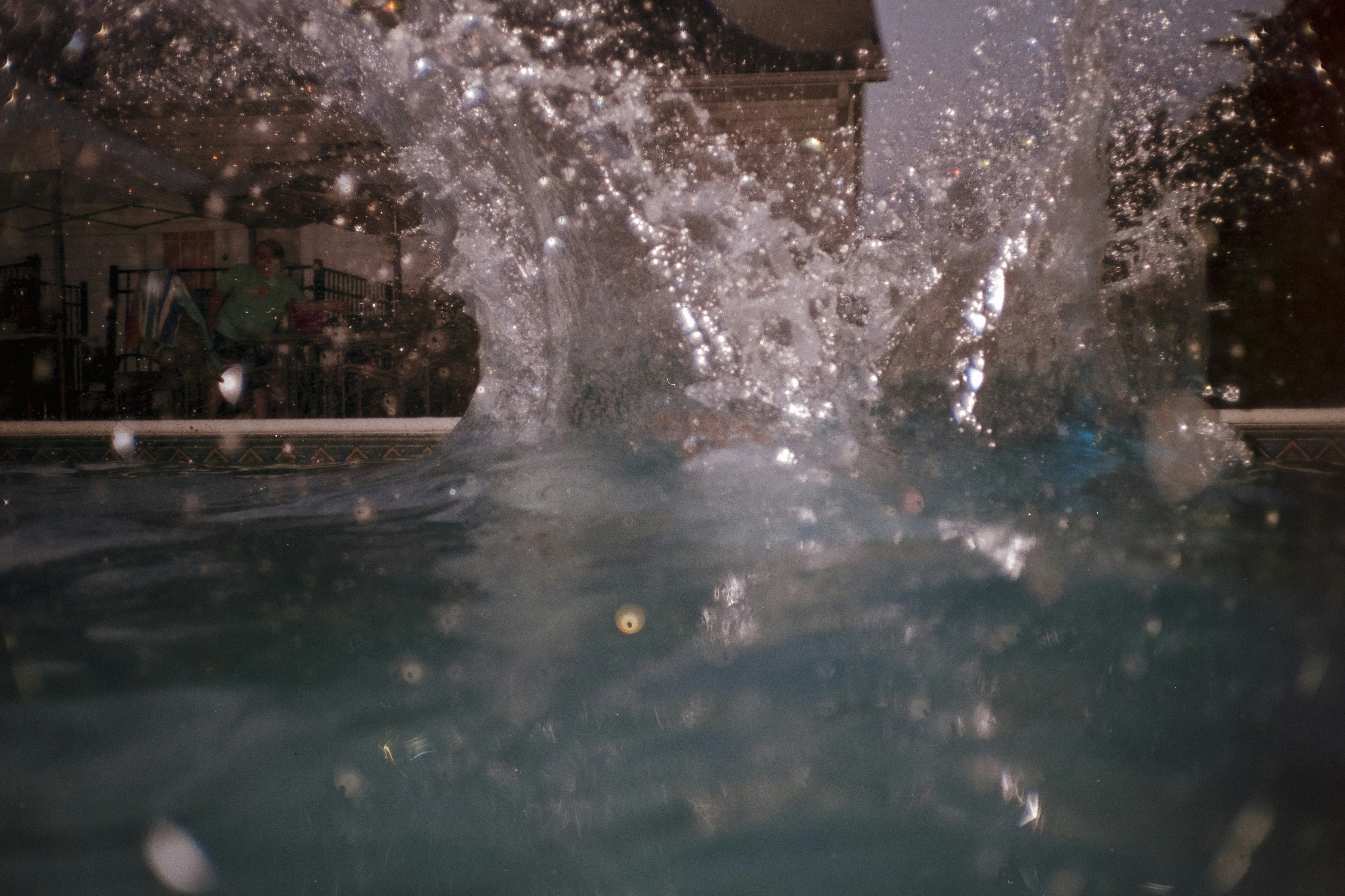 Water splashes erupt from a pool at night, with dynamic droplets frozen mid-air and blurred background lights.