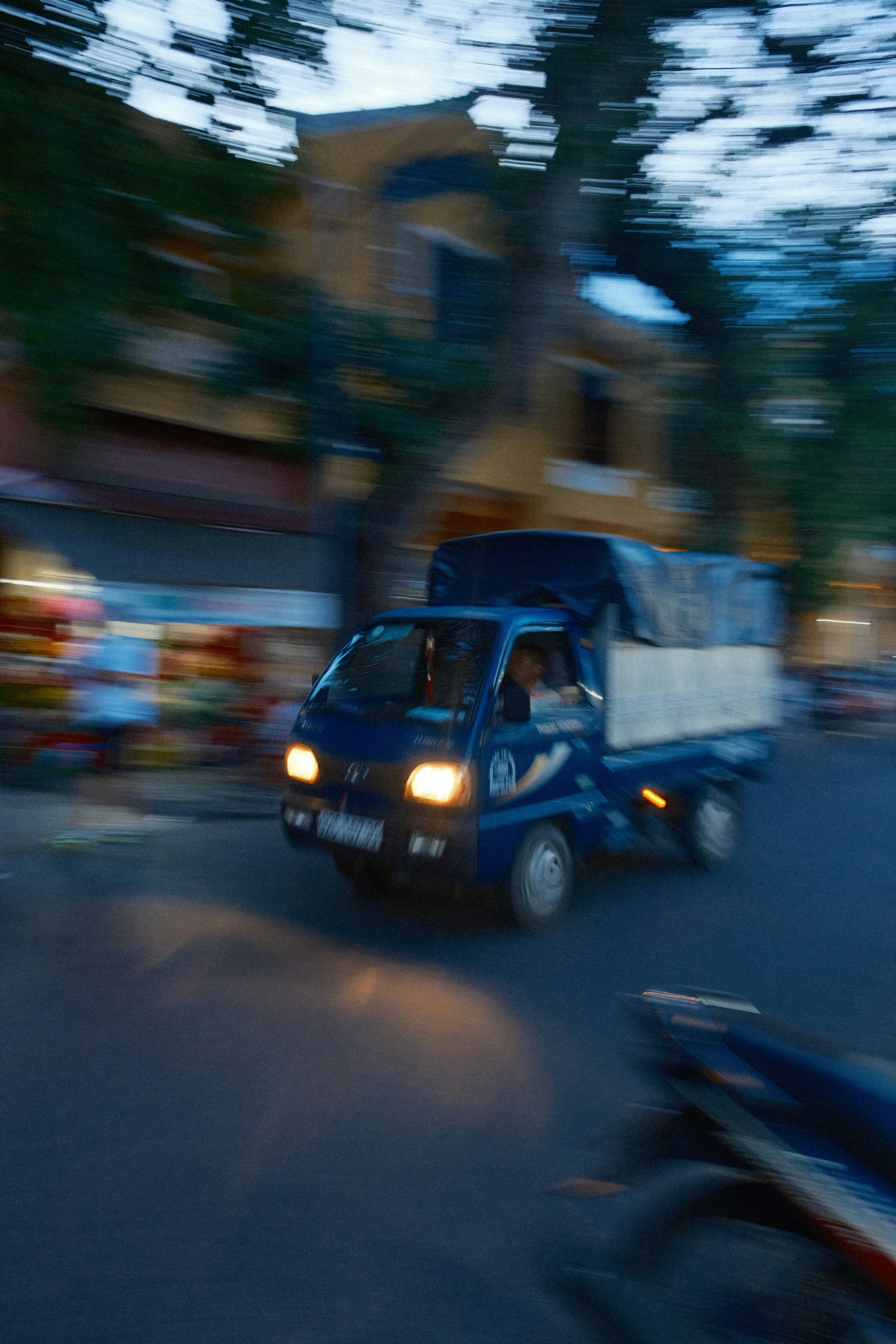 Blue courier truck cuts through a hazy blur of evening streets