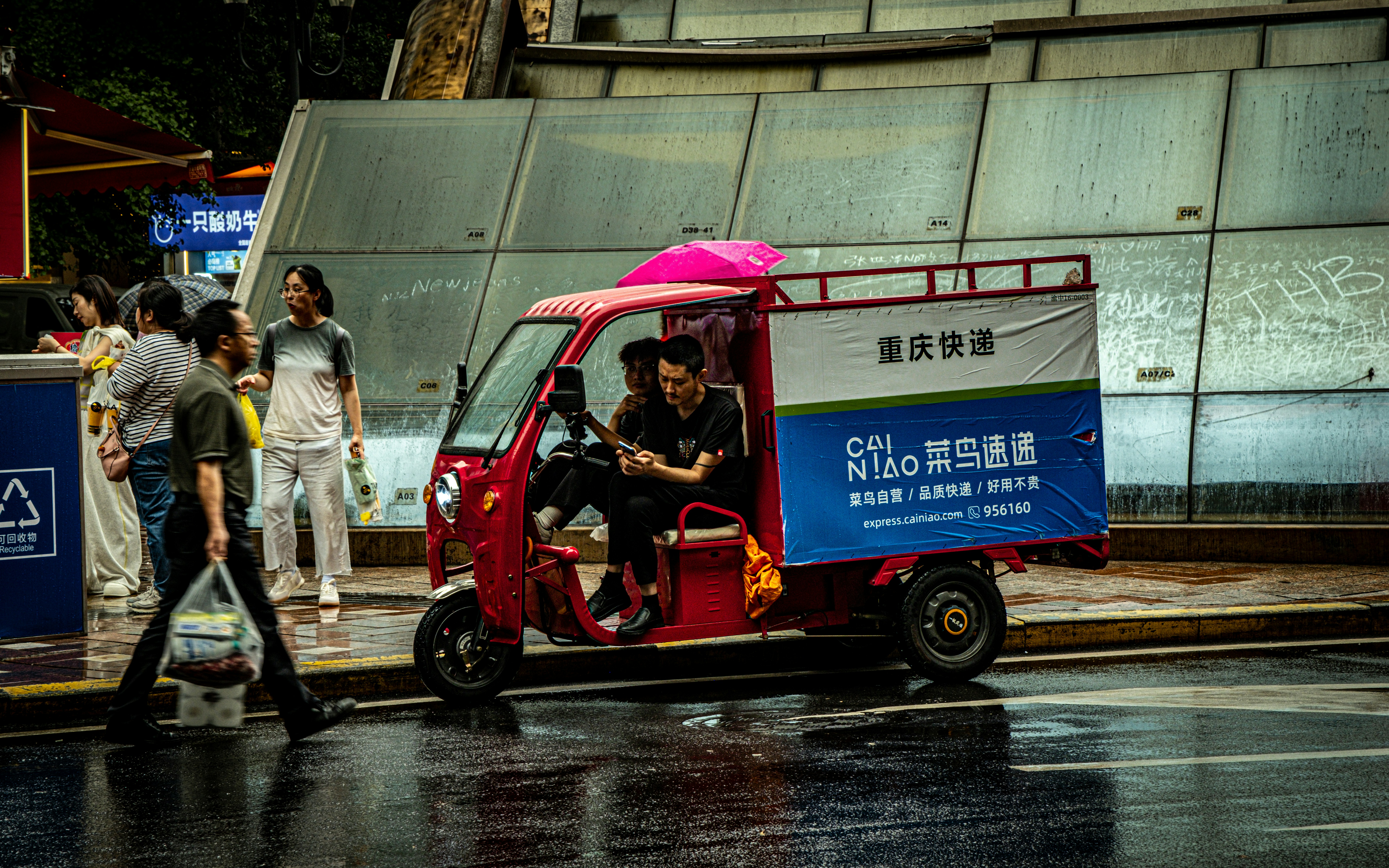 Bright pink-capped cargo trike in a rain-soaked urban street