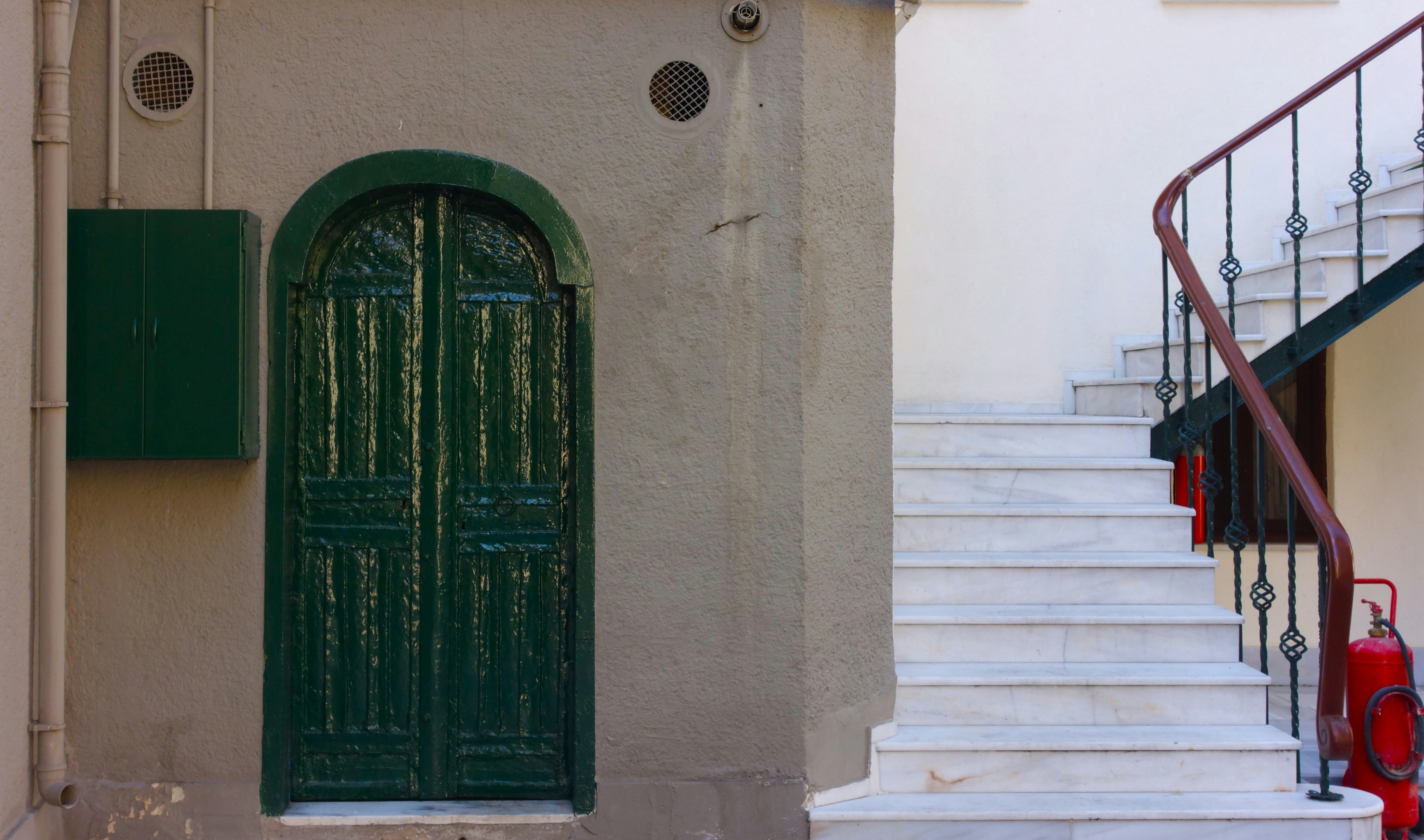 Green door on a sunlit alley with white staircase and red fire extinguisher
