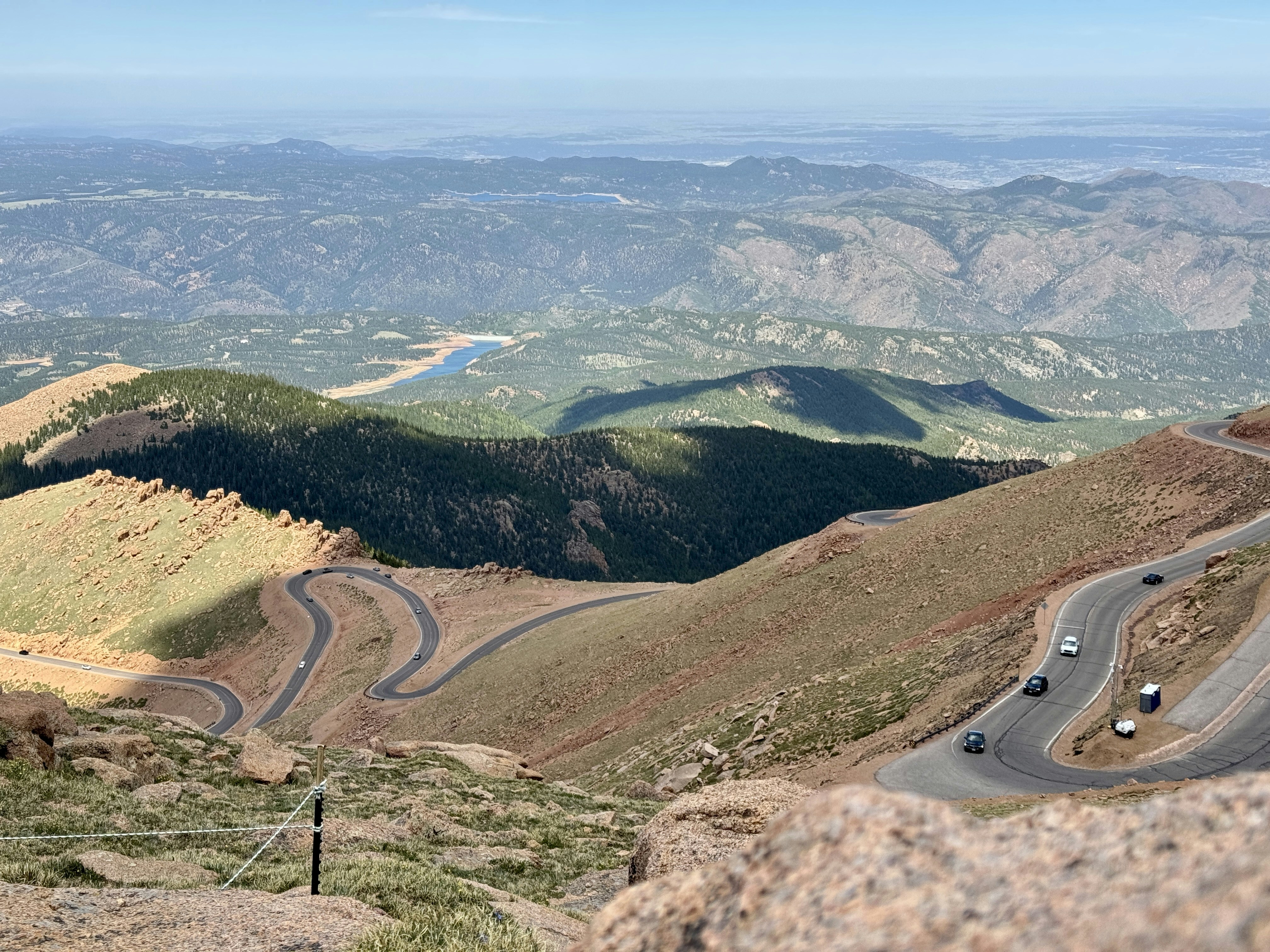 Winding mountain road cuts through arid hillside with distant valleys and blue sky. A sense of scale and terrain variation highlights the road as the focal path across the ridge. This is a landscape photograph without logos or illustrations.