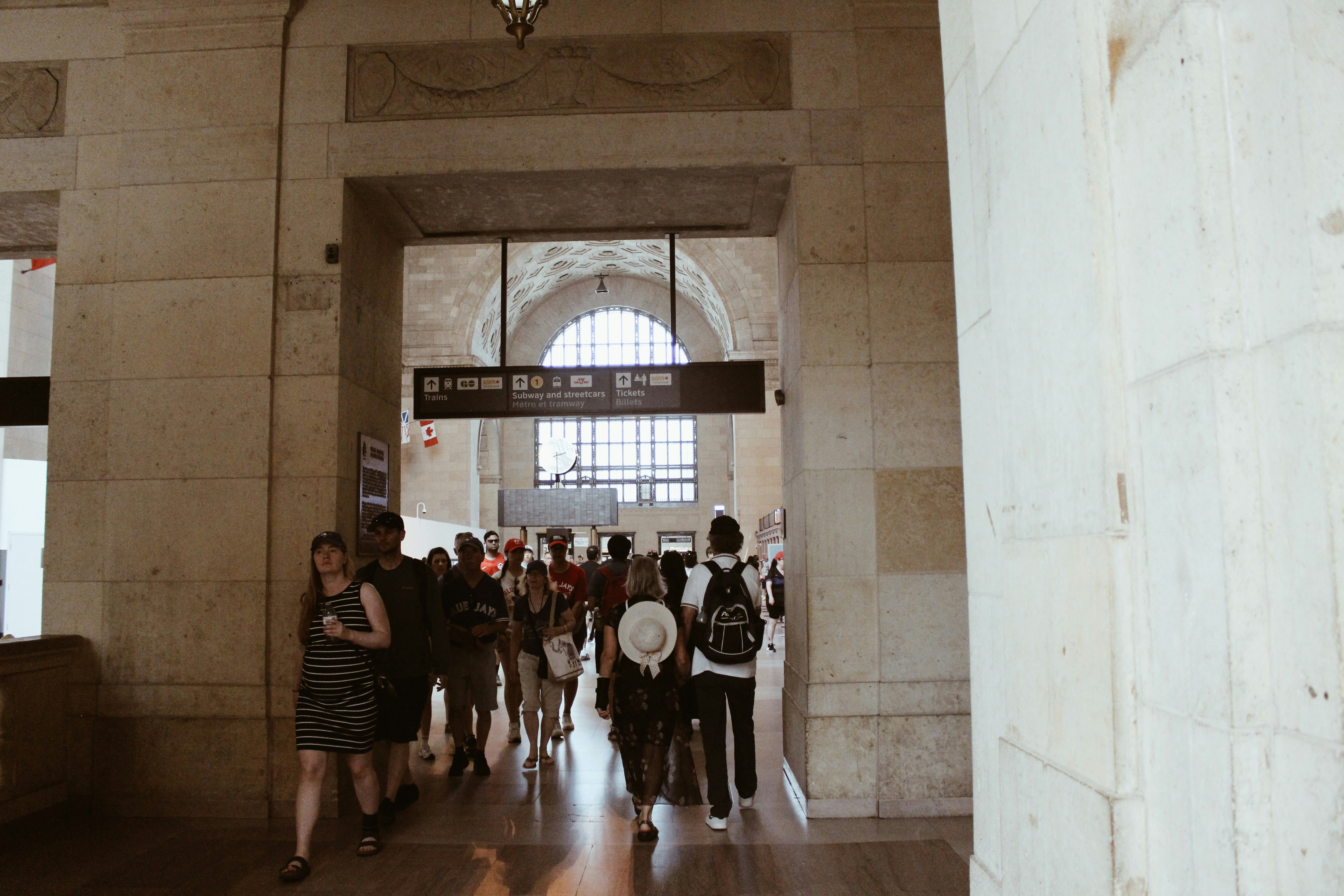 Crowd gathers and walks through a stone-arched station interior with a high, lit window in the background; a mix of tourists and locals, some with backpacks, creates a lively yet calm transit scene. (Note: photo depicts a public space.)