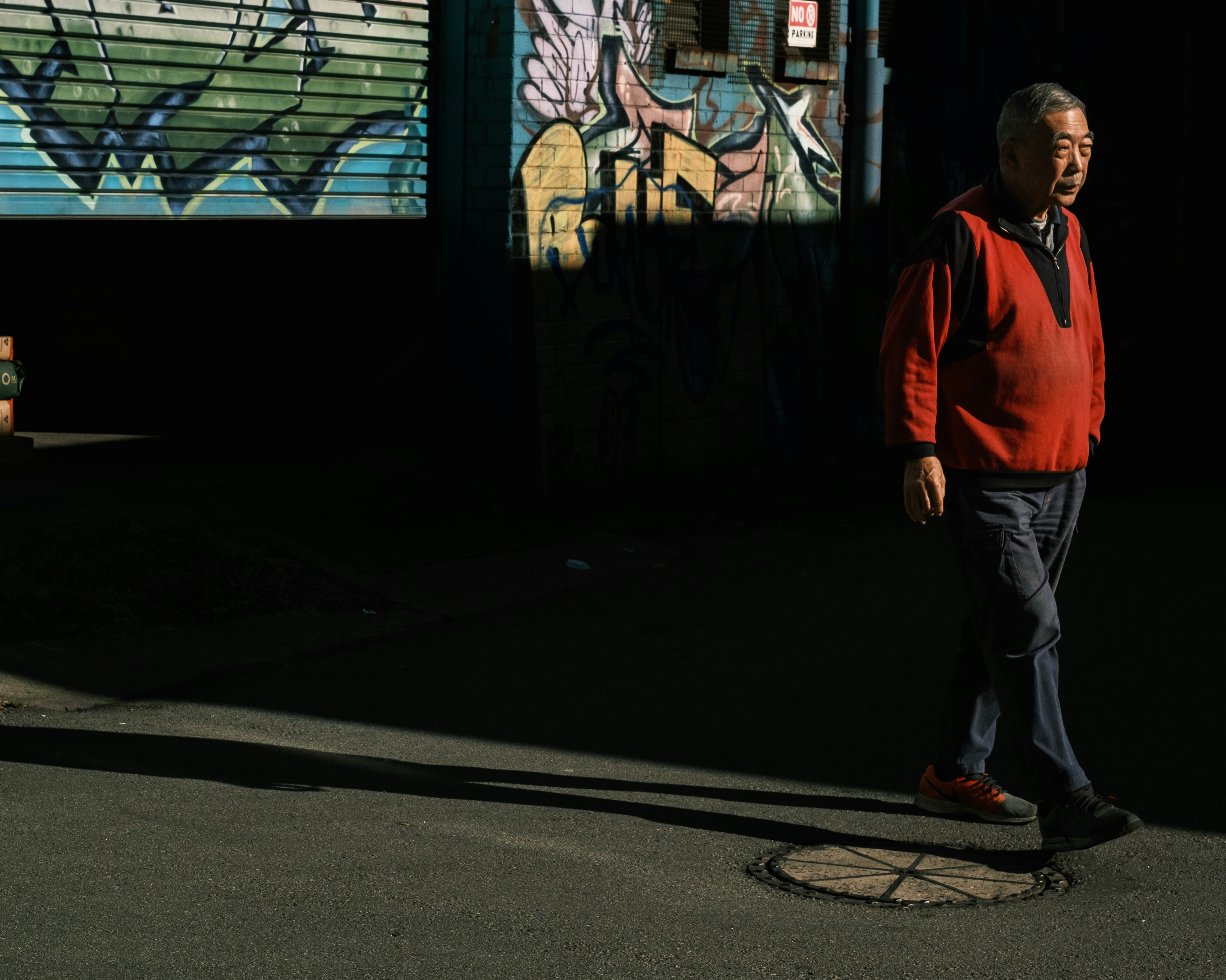 An older man in a red jacket walks past graffiti.