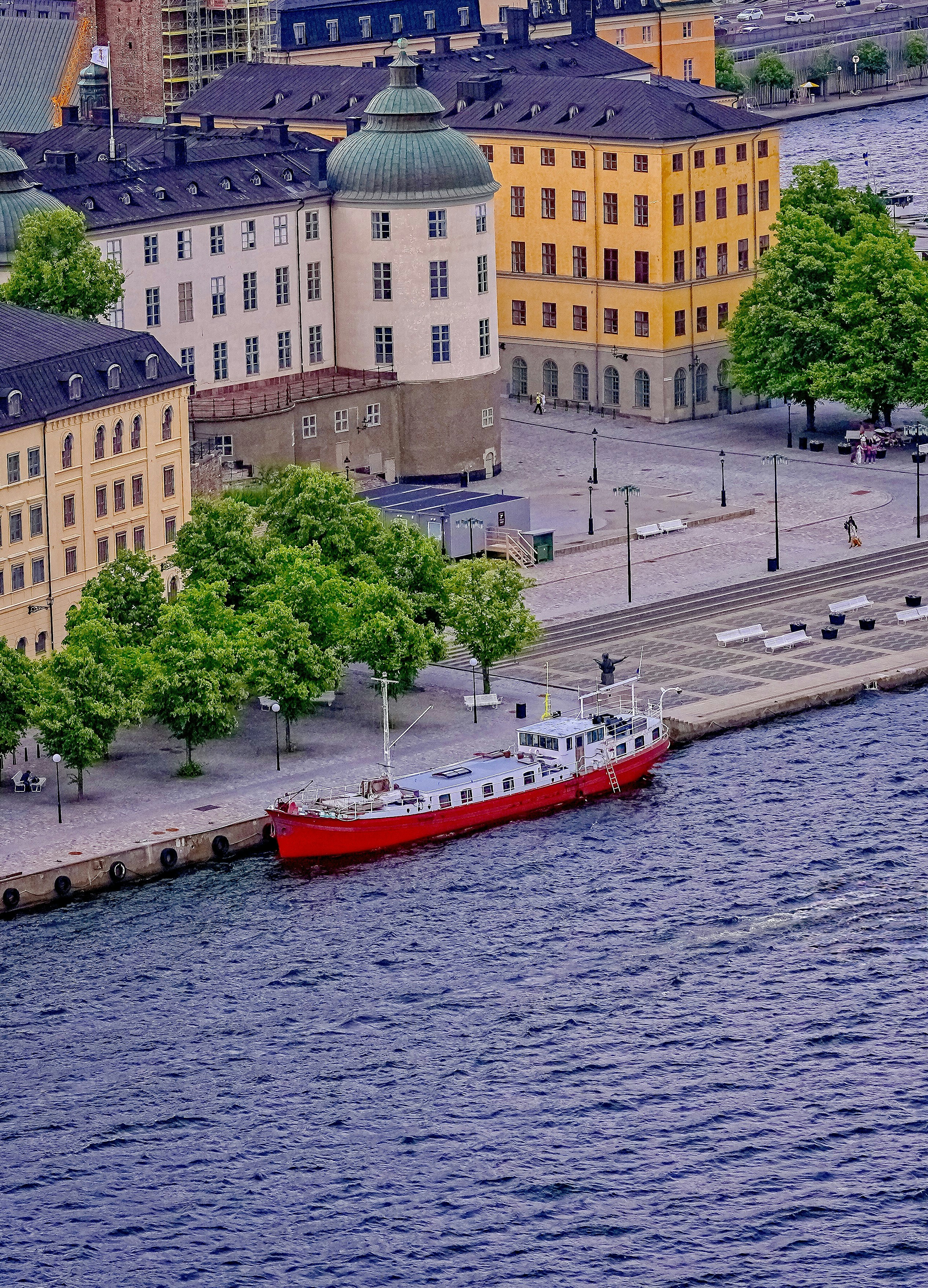 Red Vessel Skims the Waterfront Between Historic Yellow and White Arcades