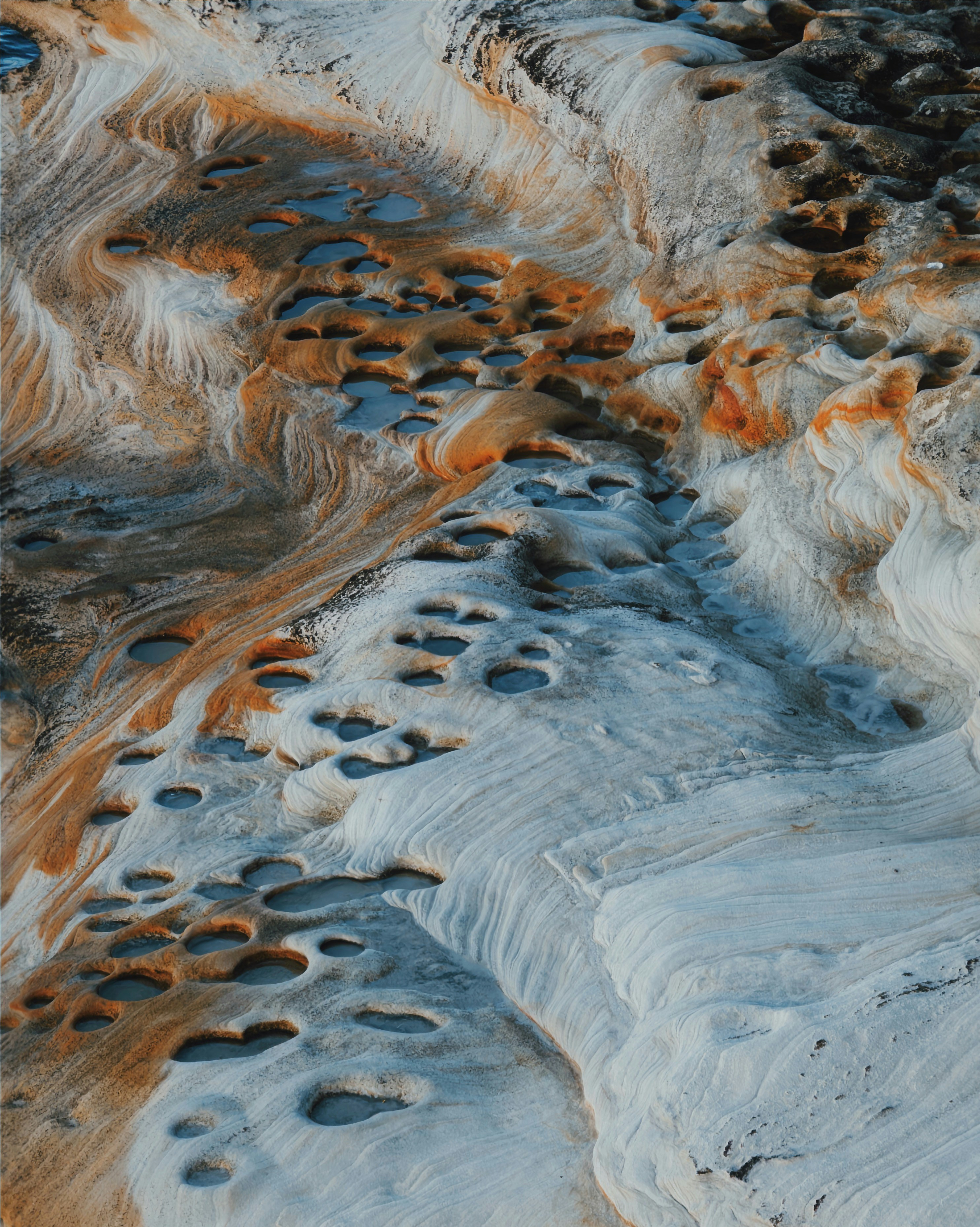 Painted rock formations with orange highlights and smooth, wavy textures; a geological landscape captured from above. This is a natural rock surface.