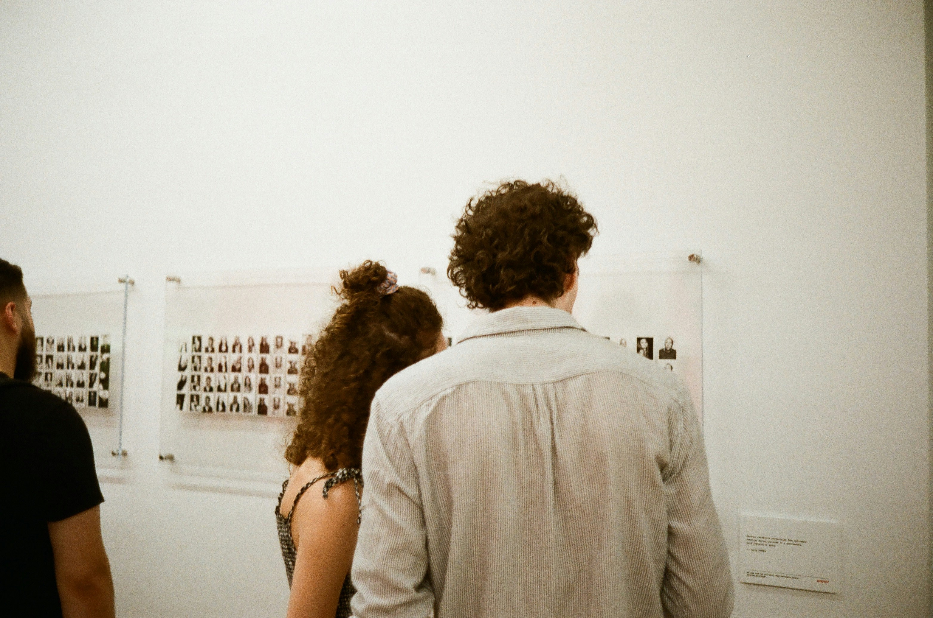 Two people viewing small pictures on a white gallery wall.