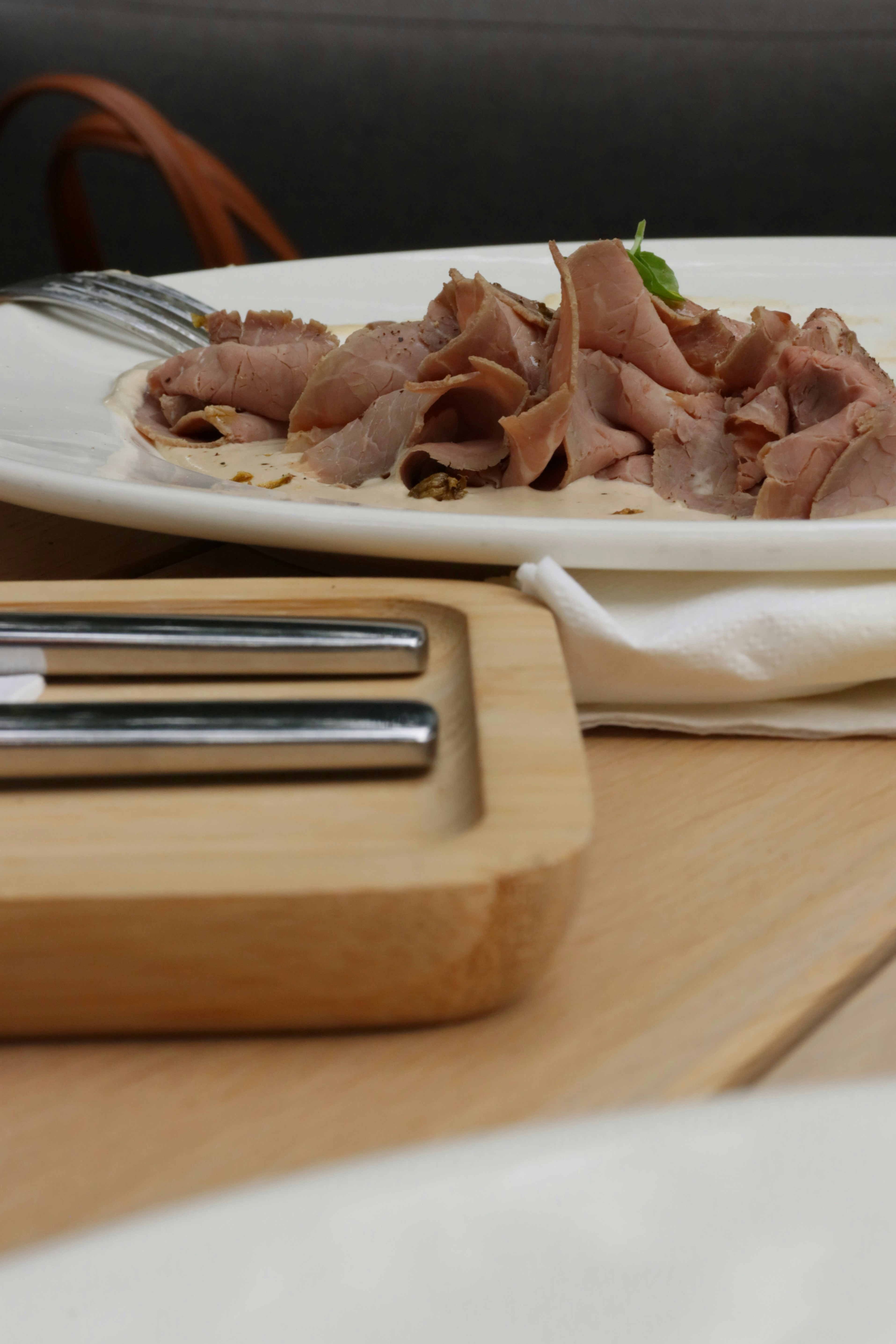 Sliced roasted meat on a white plate with a wooden knife tray in a casual dining setup