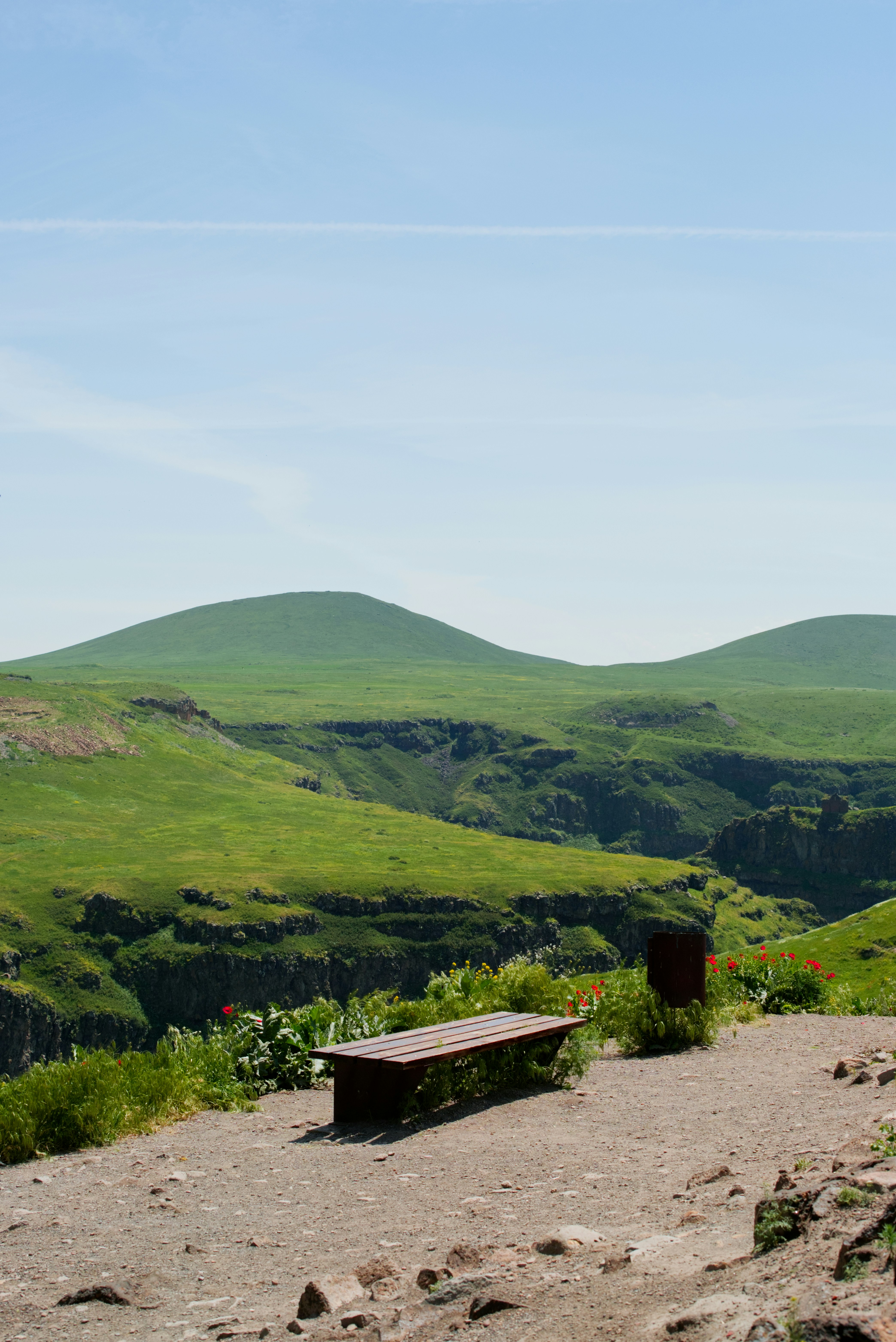 Quiet overlook: a lone bench faces emerald hills under a clear blue sky
