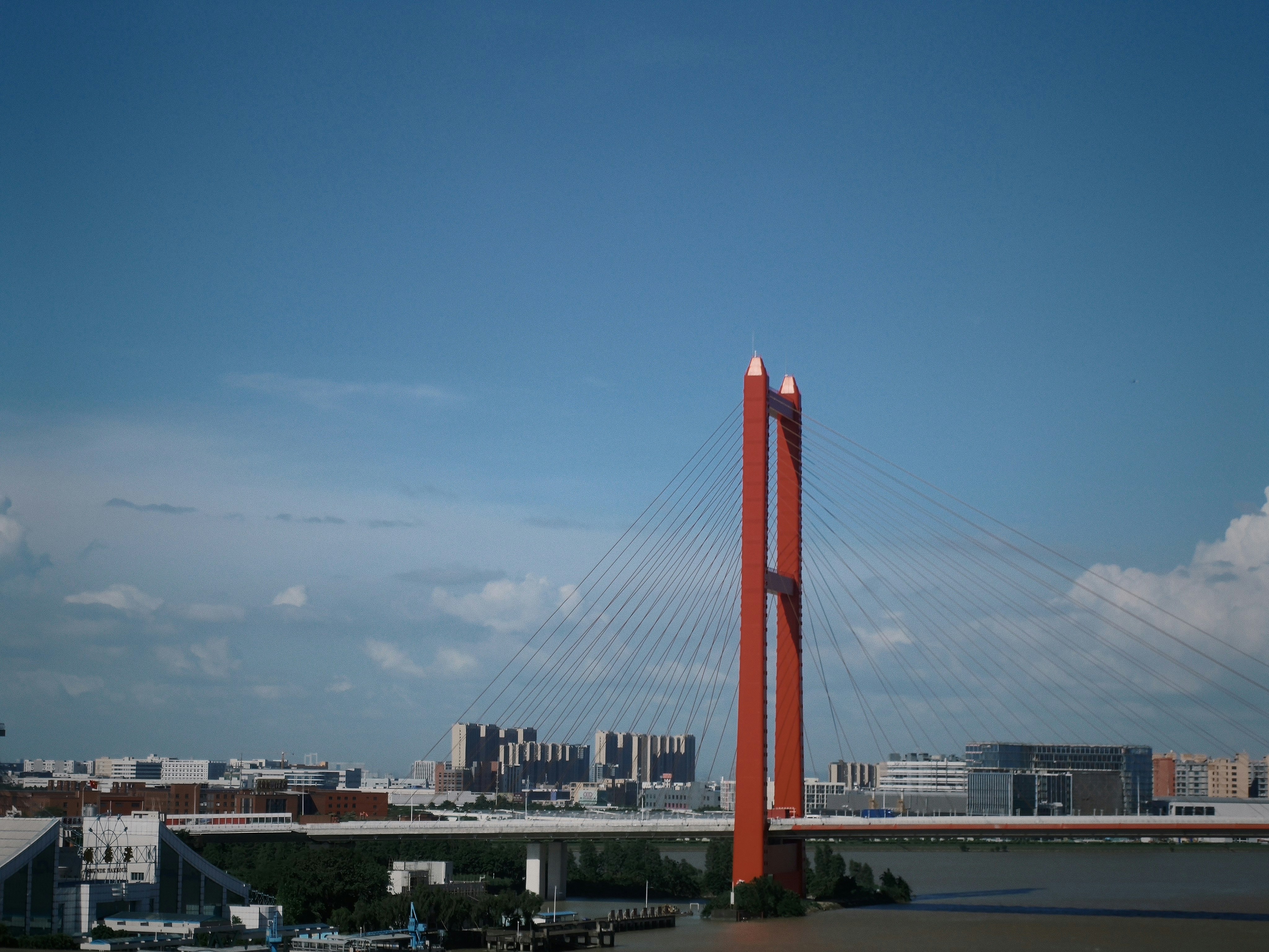 Red bridge pylon, cityscape, and river under a blue sky.