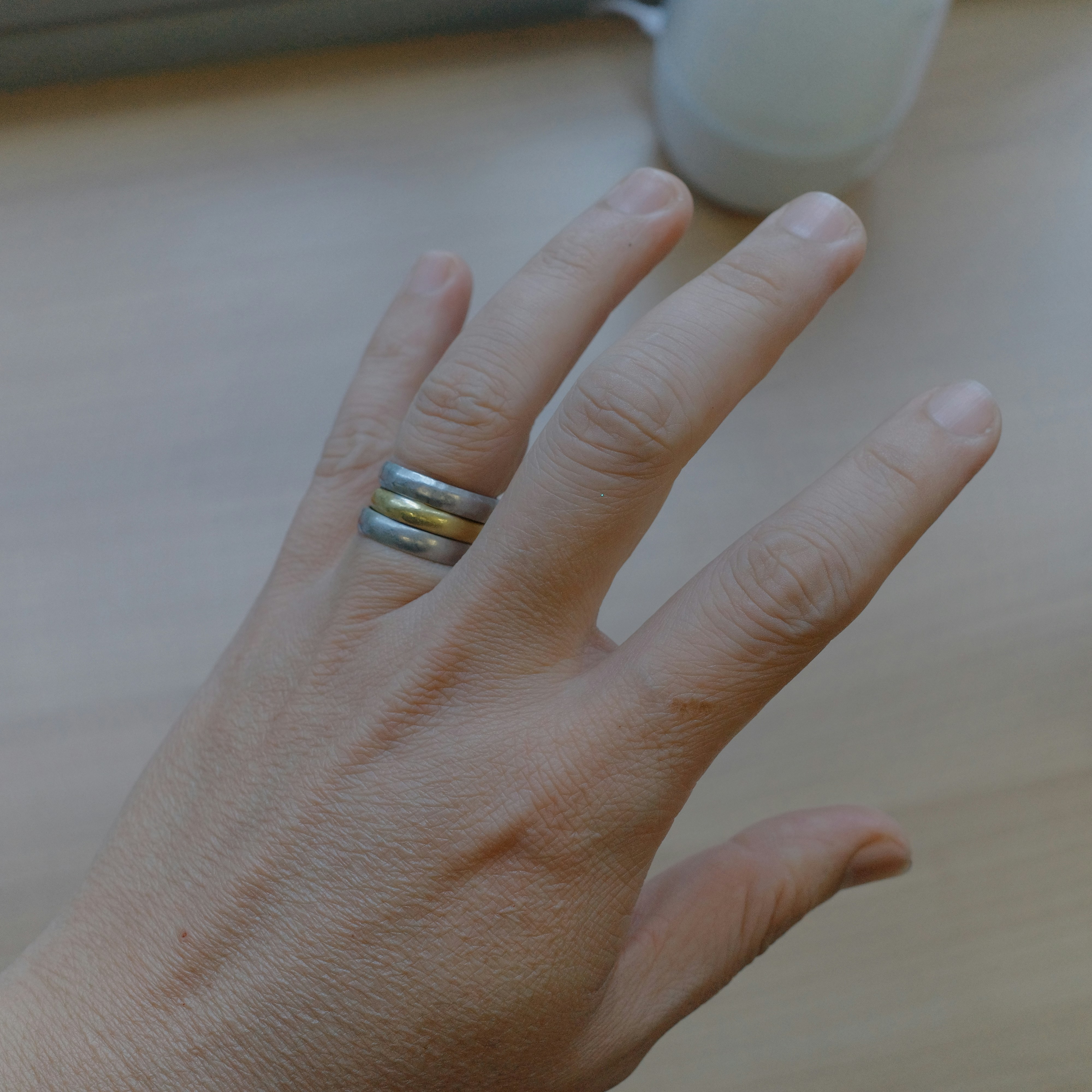 Close-up of a silver-gold ring-adorned hand resting on a wooden surface