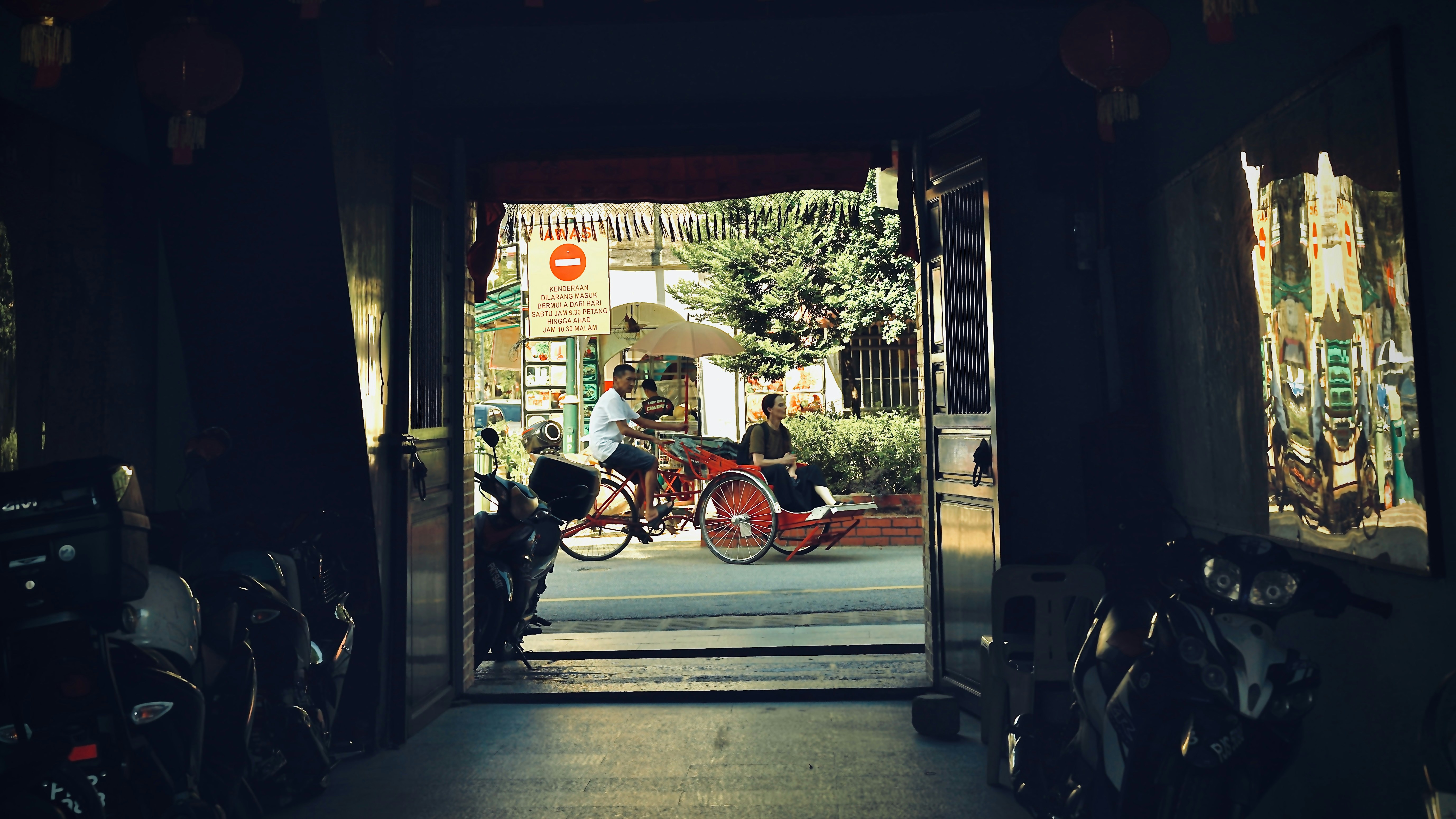Riders on a Narrow Street: A Quiet Transit Moment Through the Shop Threshold