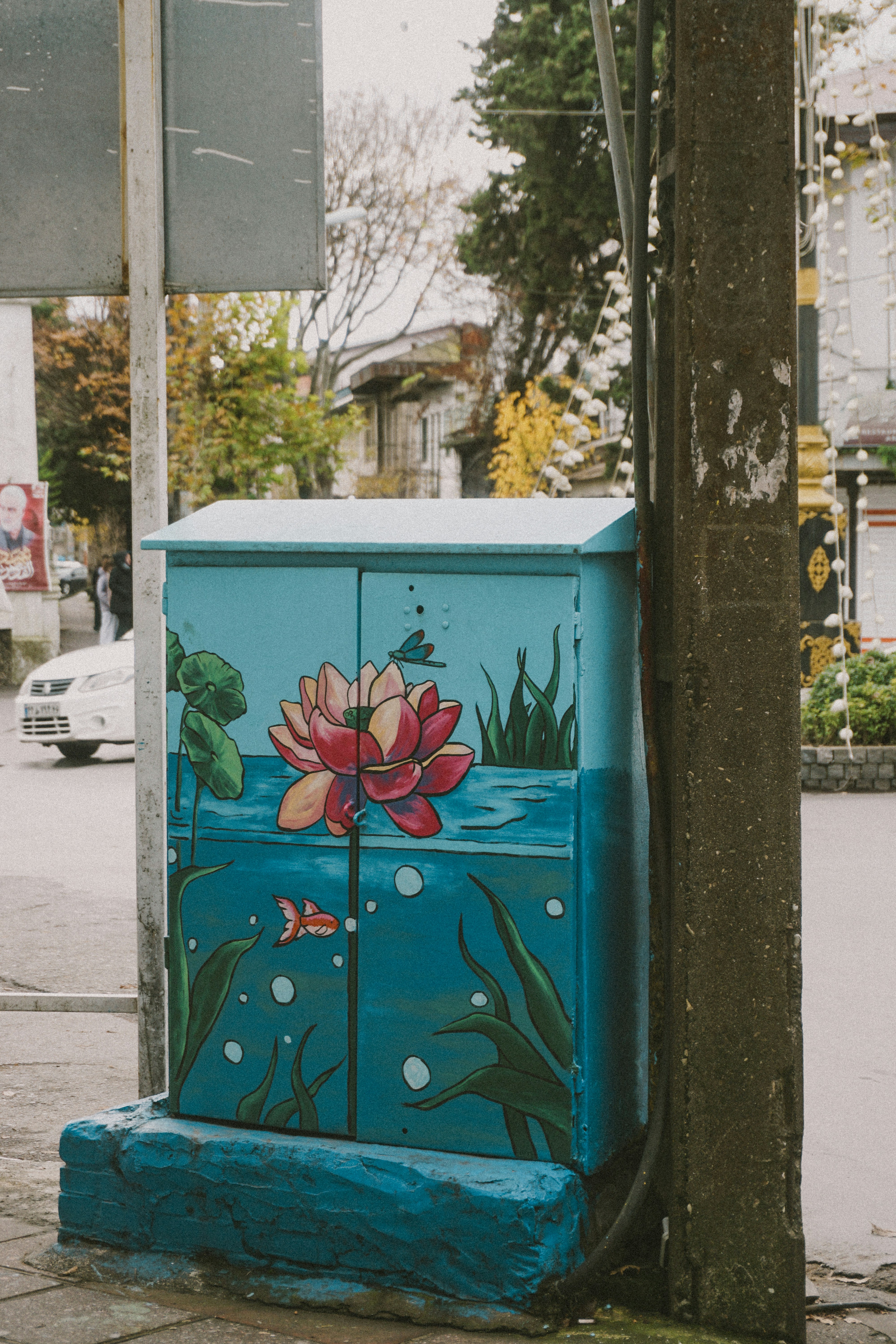 Blue Utility Box Adorned with Lotus Scene on a Street Corner