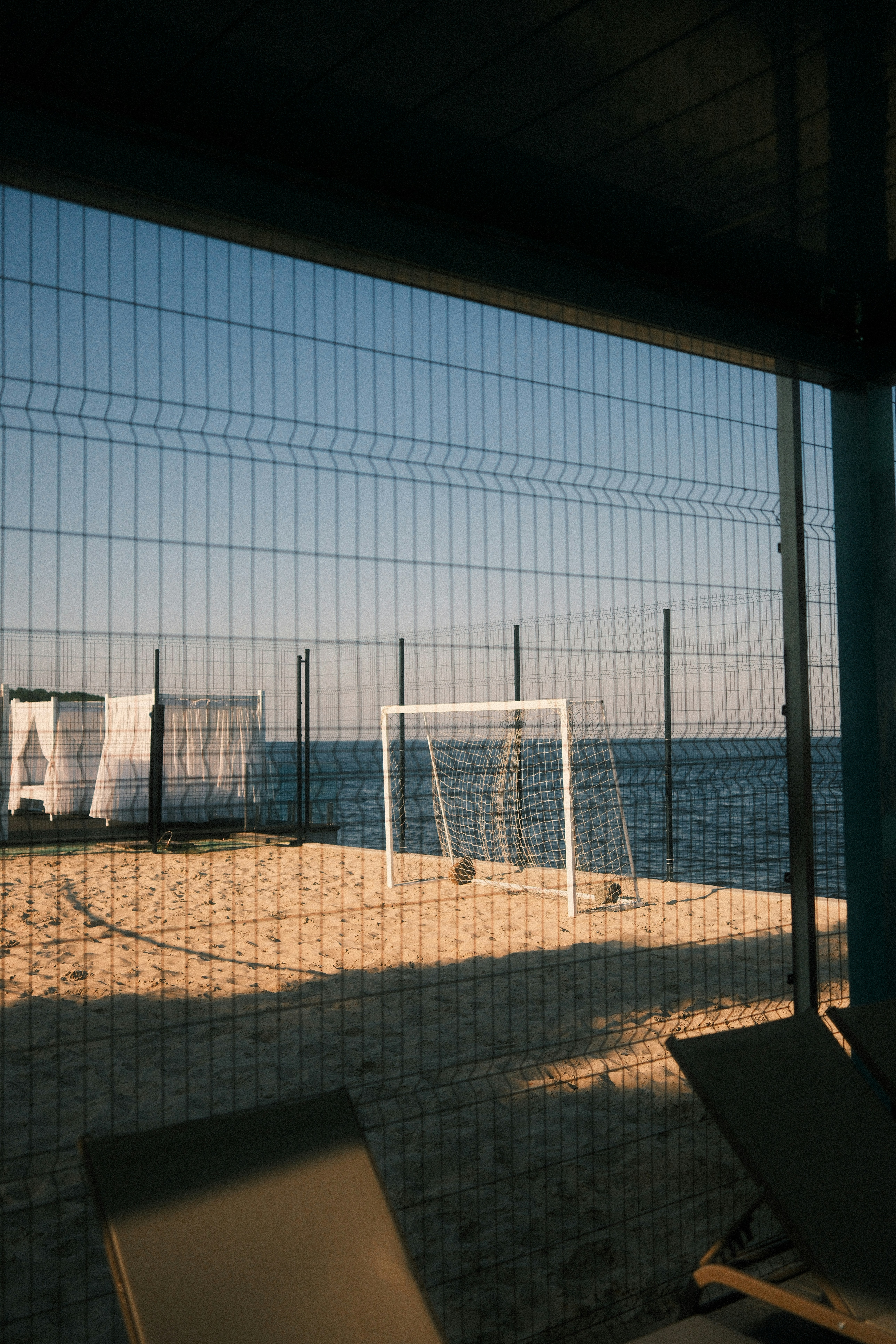 Coastal Court: A Sunlit Sand Field Through a Mesh Fence